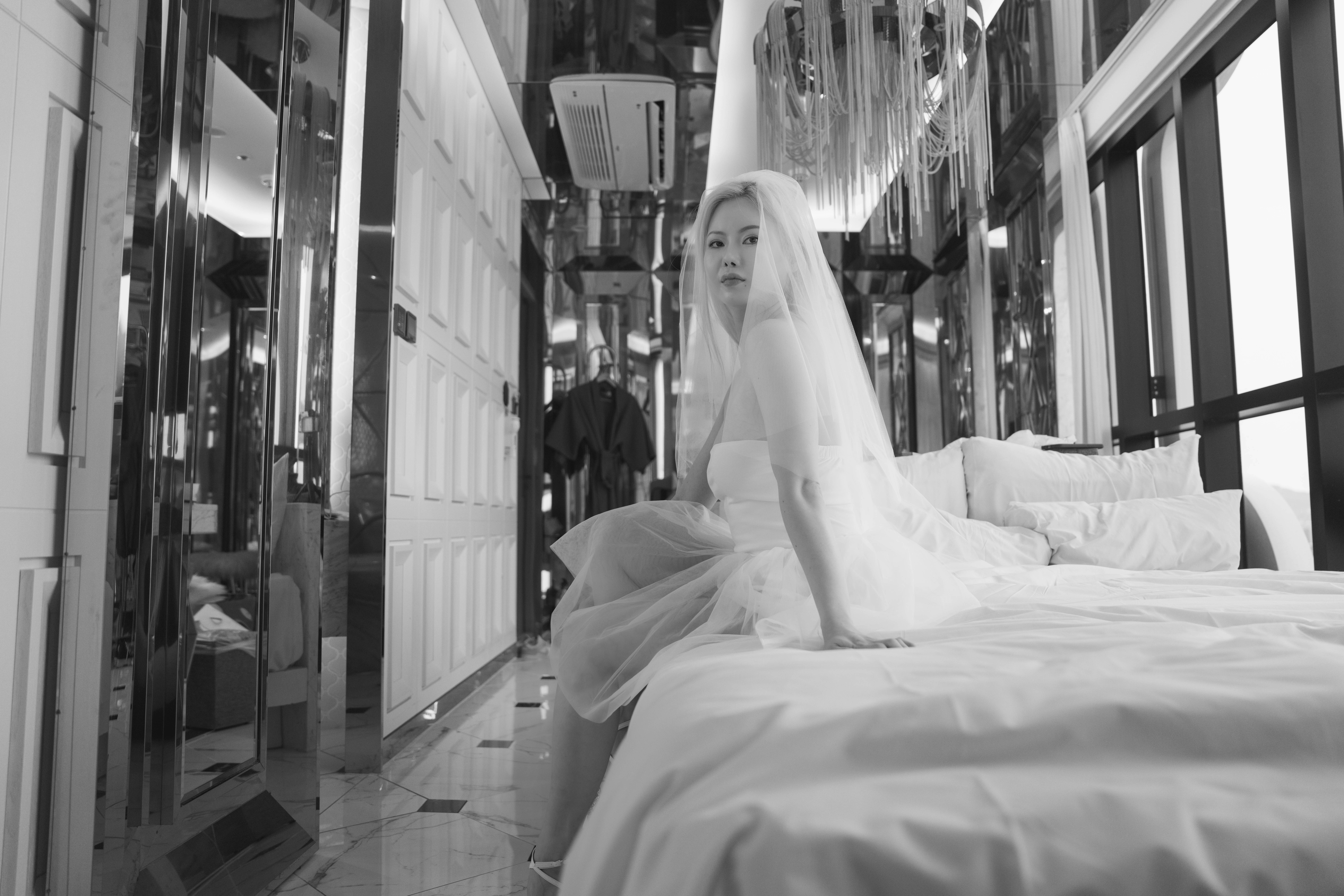 Monochrome Veil: Bride Pauses on a Bed in a Hotel Suite