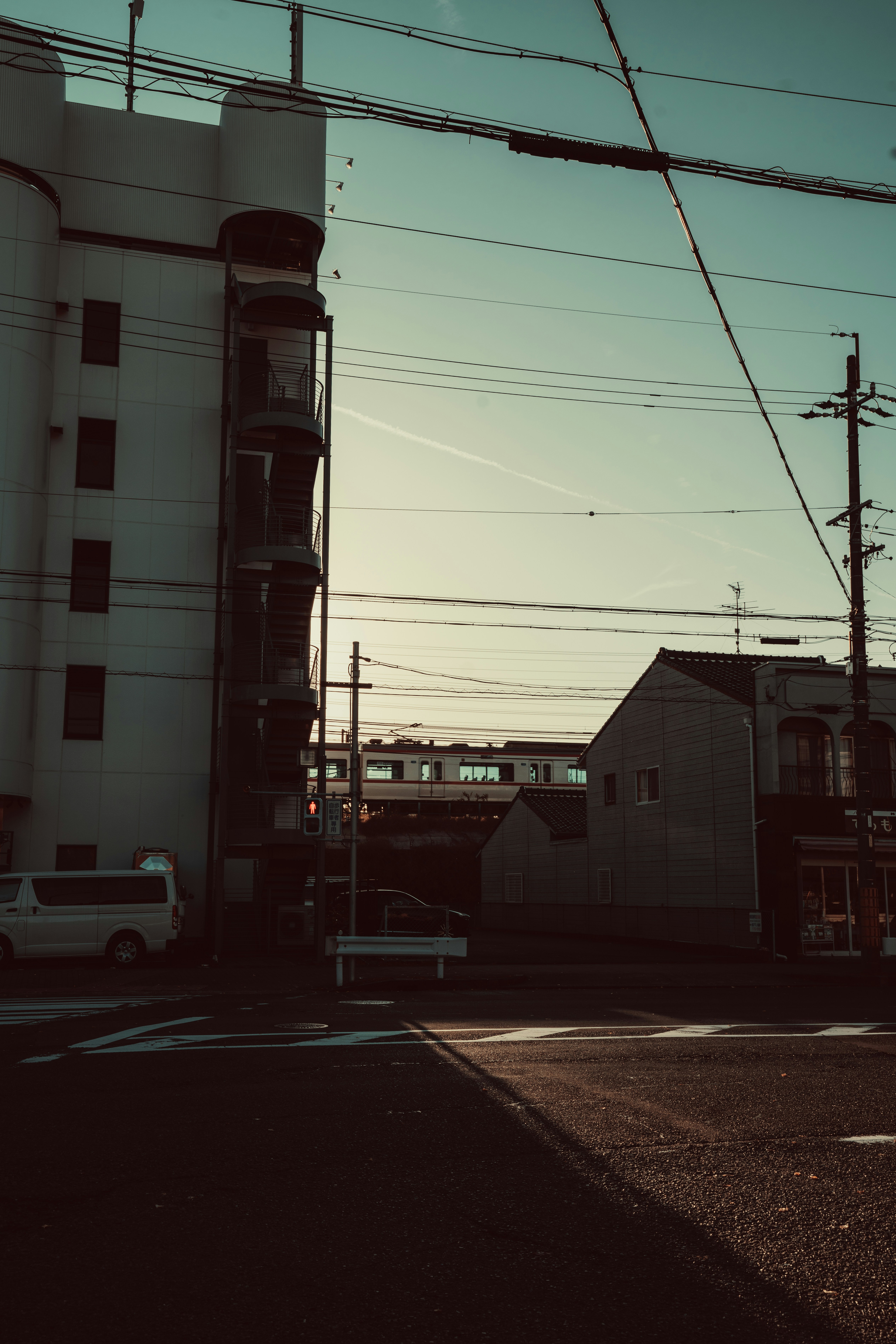Silhouetted buildings and power lines against a dusky sky, with a train visible in the background. The scene captures the essence of urban life transitioning into evening.
