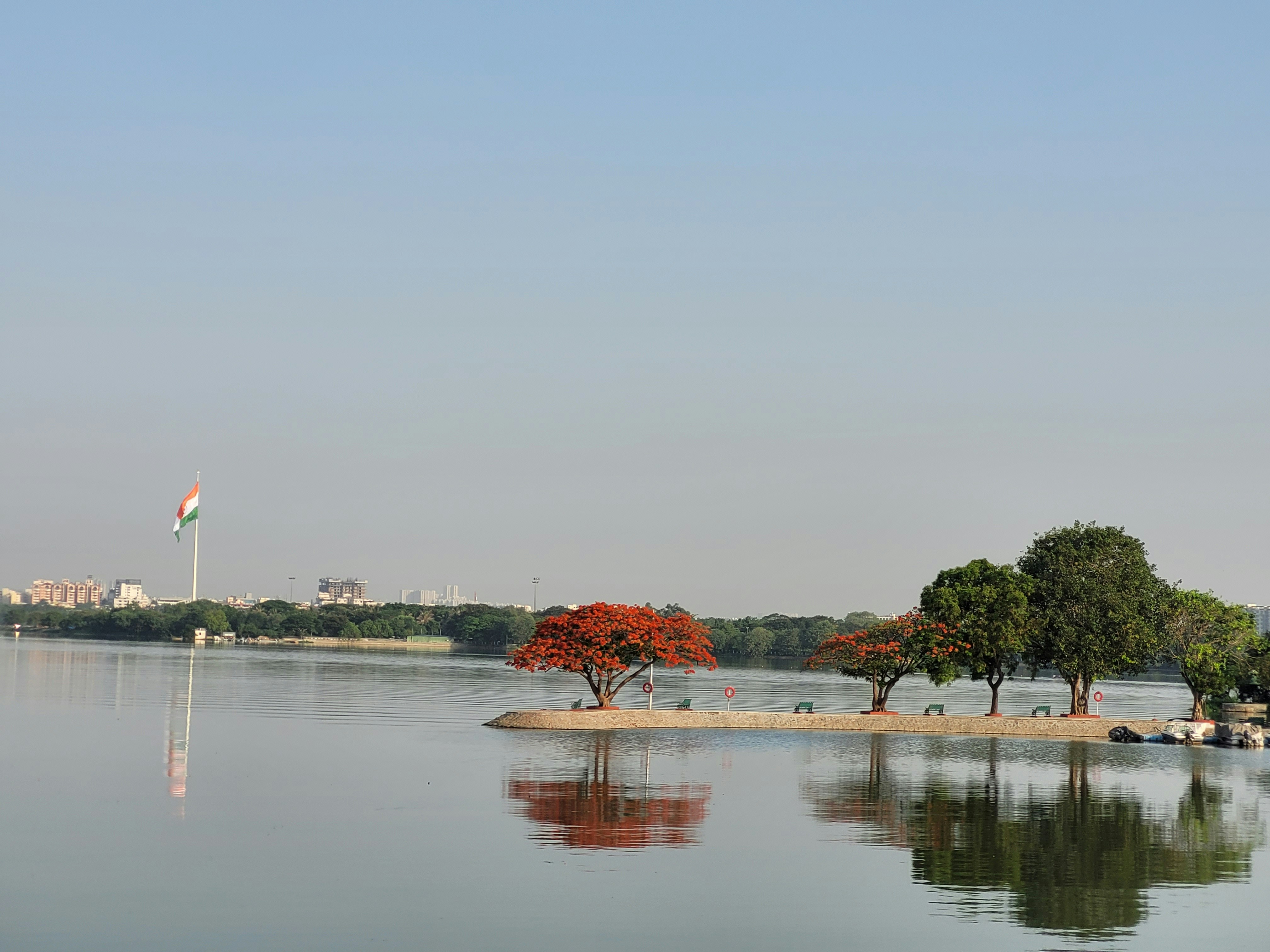 Calm lake with small tree-covered island reflecting in the still water under a clear blue sky.