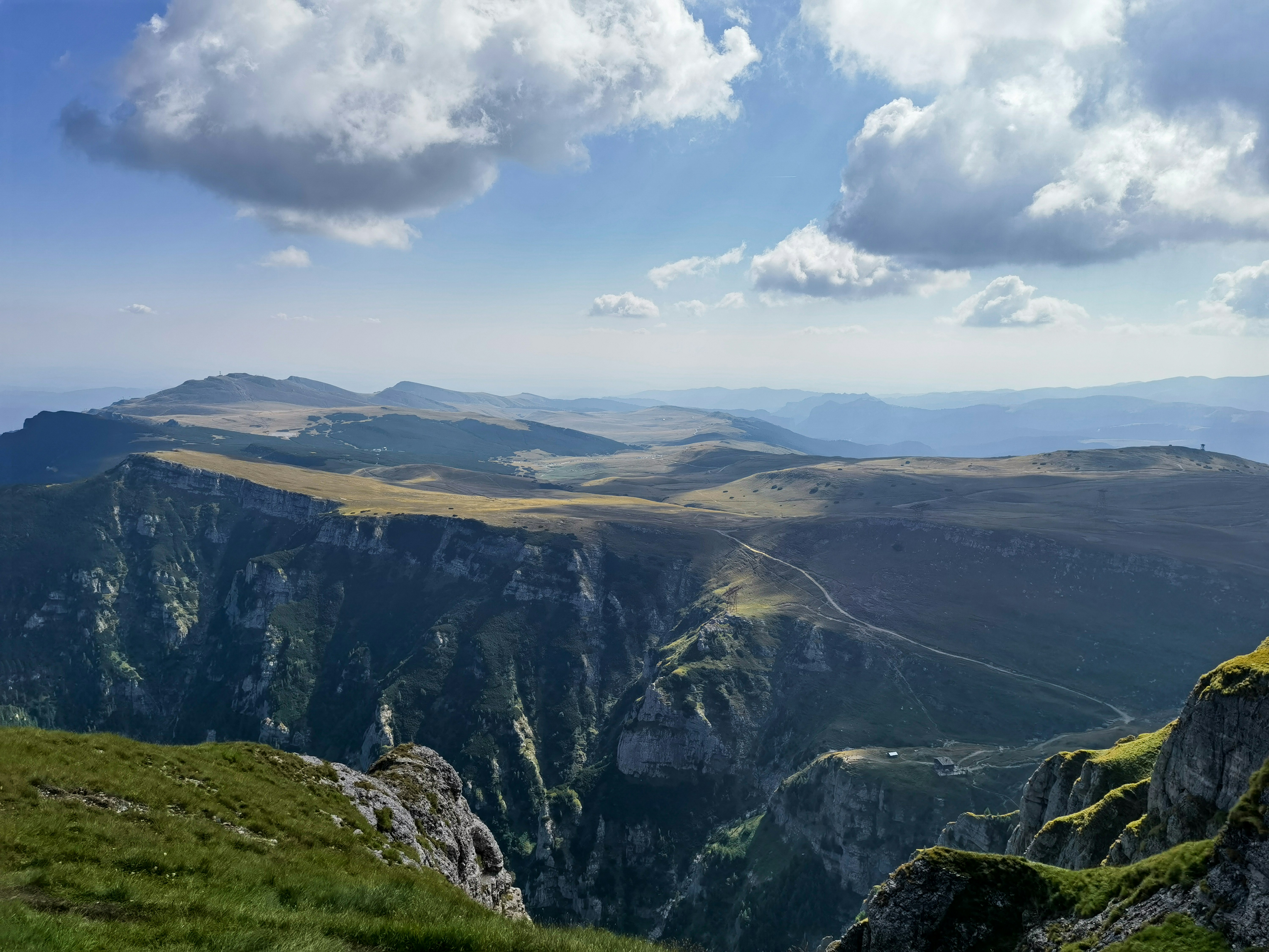Expansive view from a mountain peak overlooking rugged cliffs and distant rolling hills with a dramatic sky. 