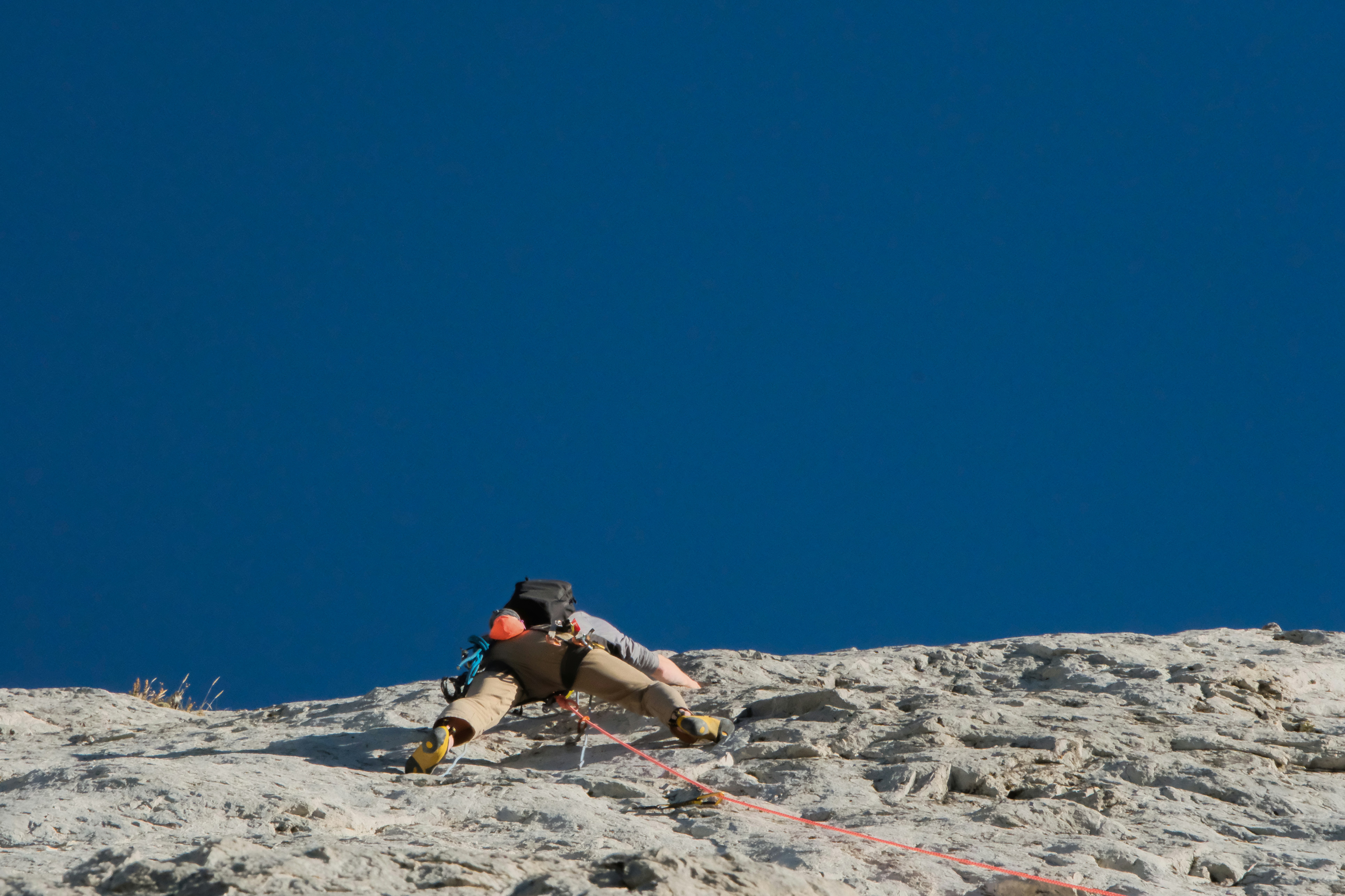 Cliff Ascent: A climber's deliberate ascent under a vast blue expanse