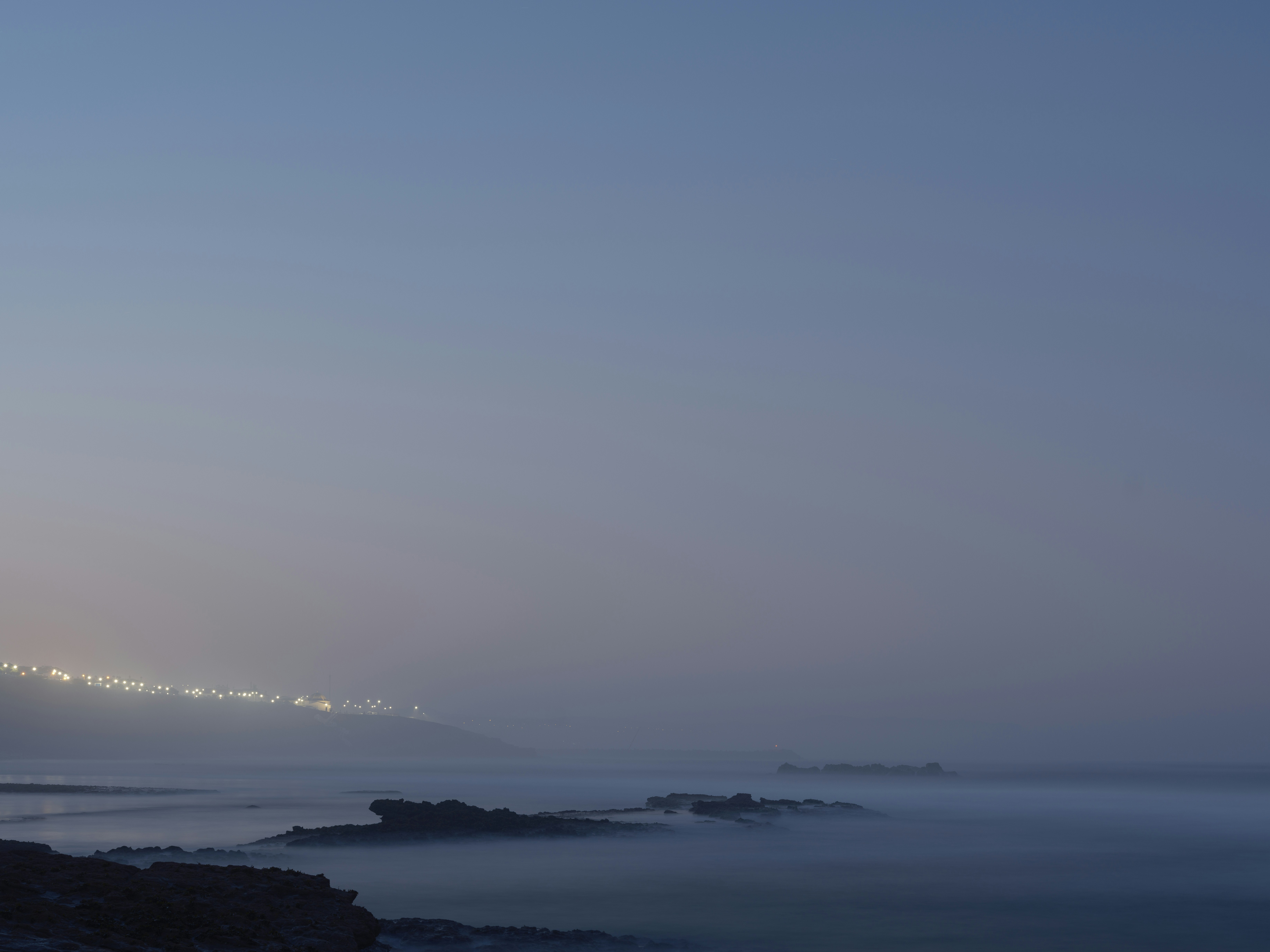 Dawn over a Misty Coastline with Distant Lights