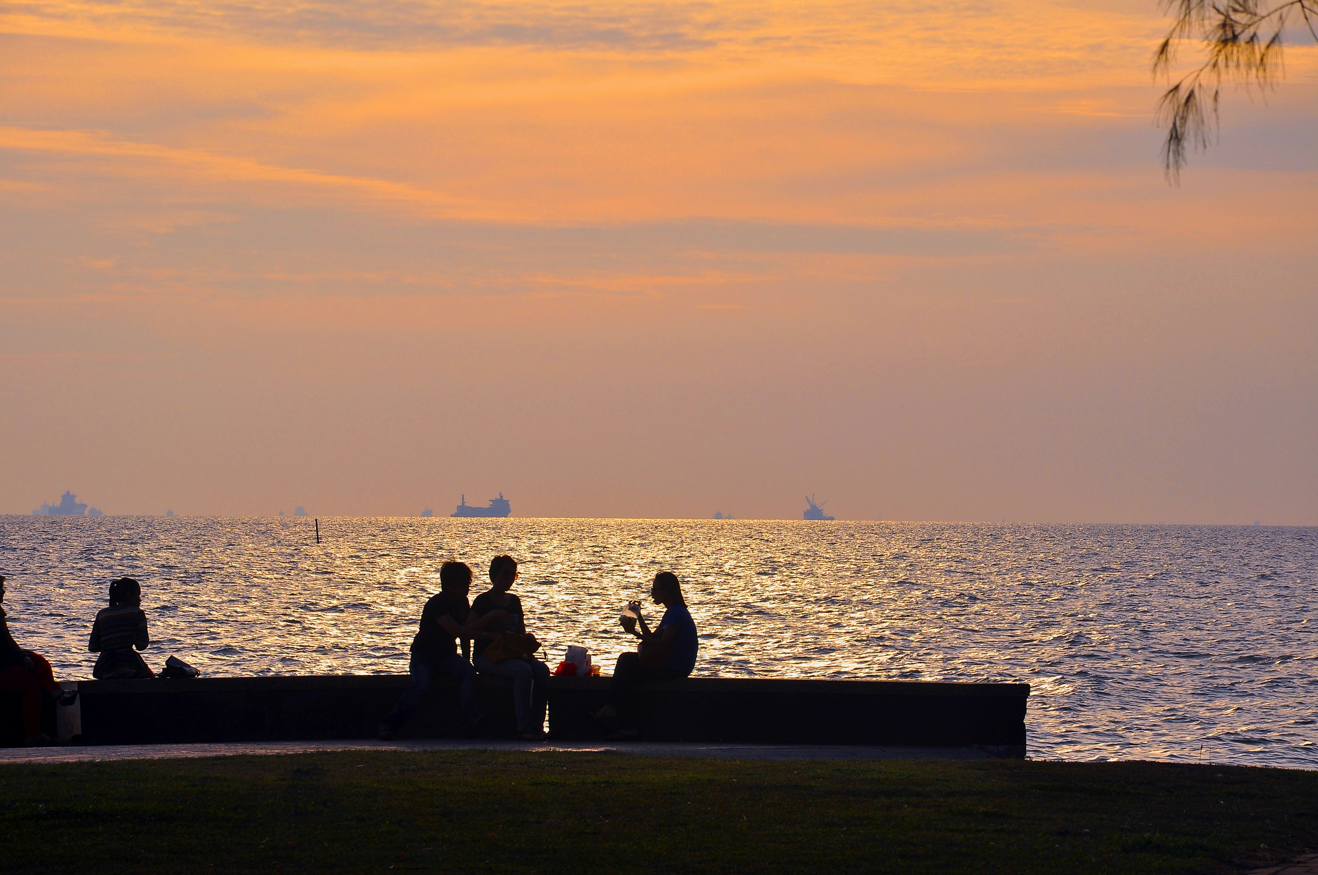 Silhouetted figures relaxing on a beach as the sun sets over a calm sea.