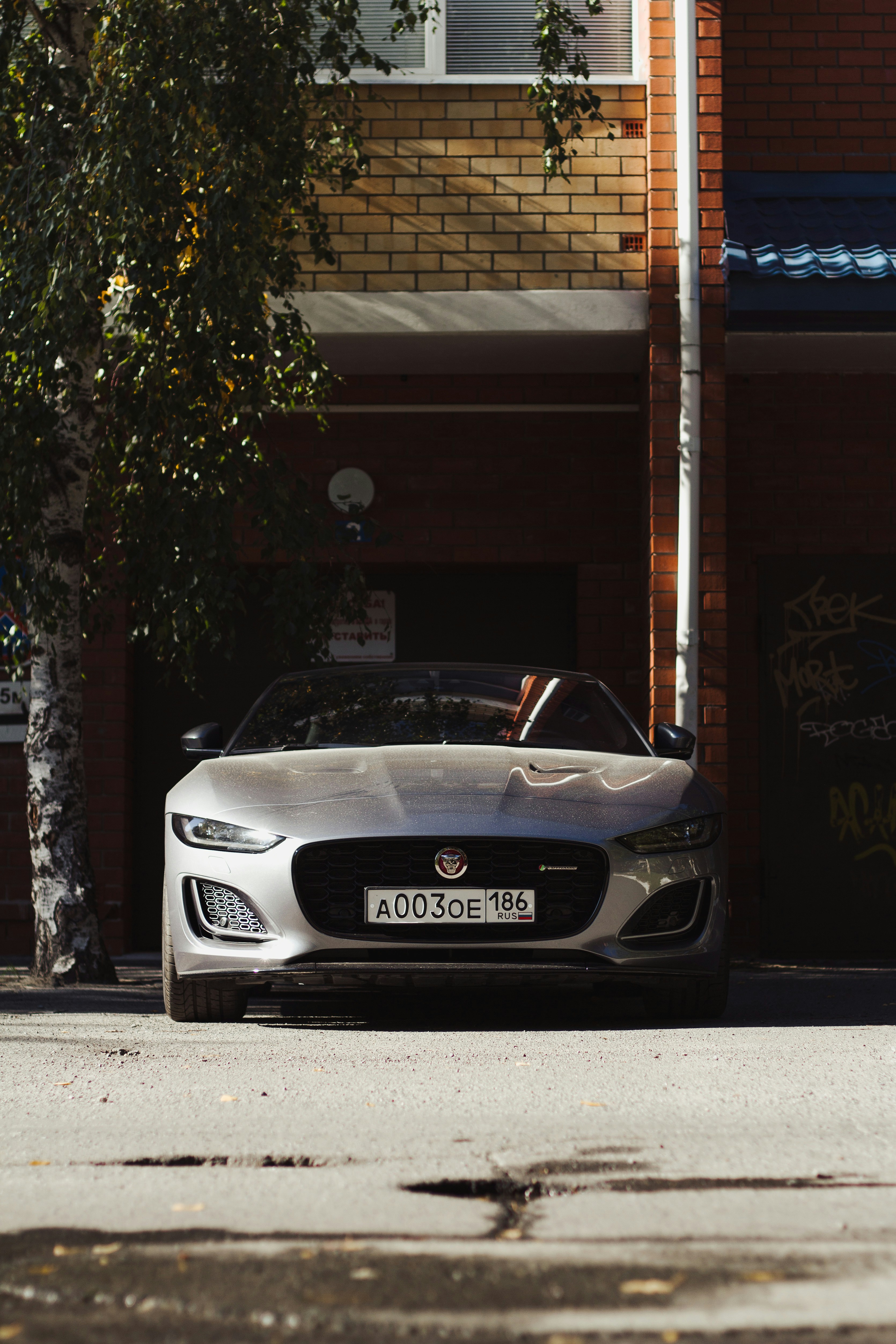 Silver Jaguar Parked Under a Brick-Walled Arch in a Sunlit City Street