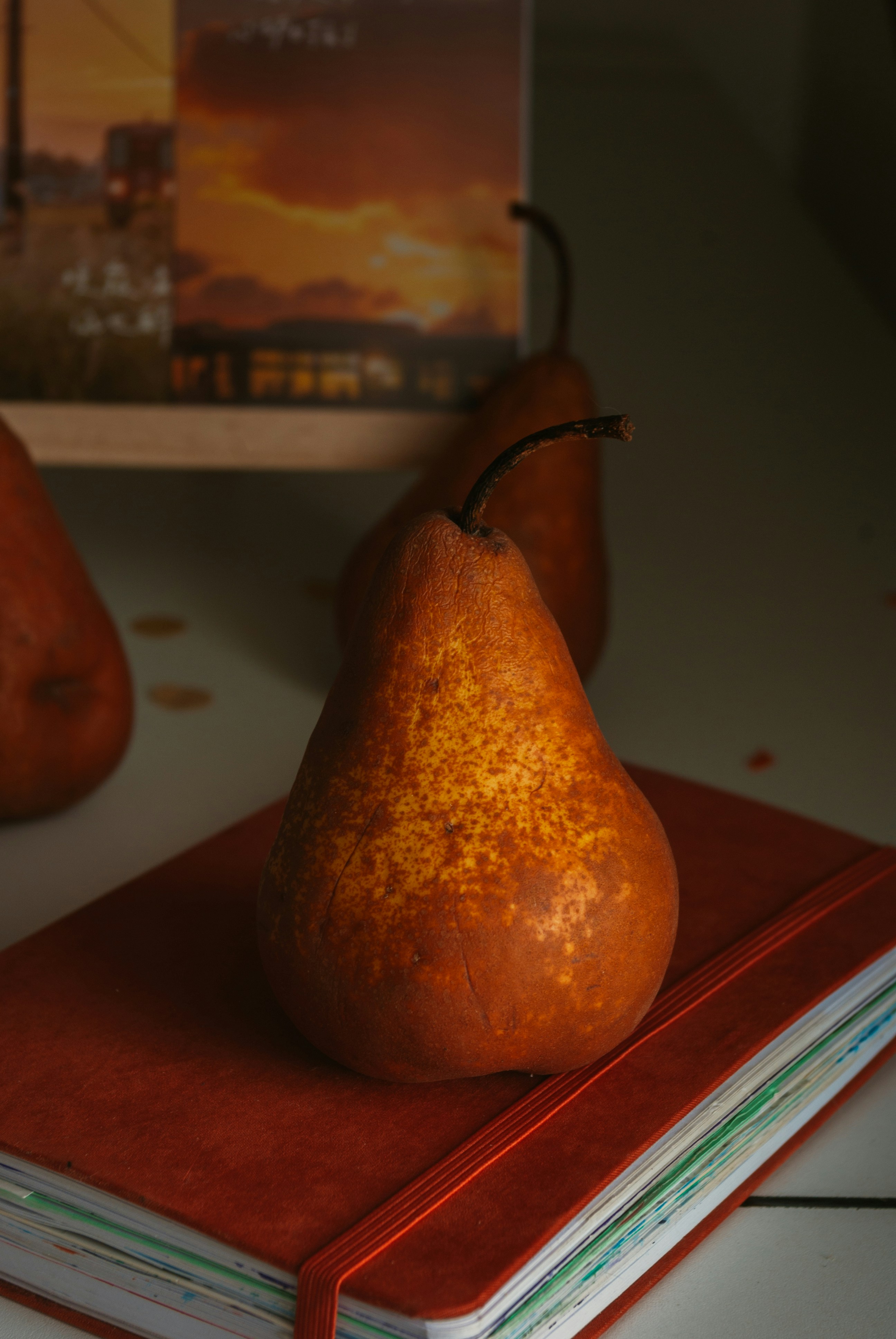 Amber Pear on a Red Notebook: A Quiet Desk Still Life in Warm Light