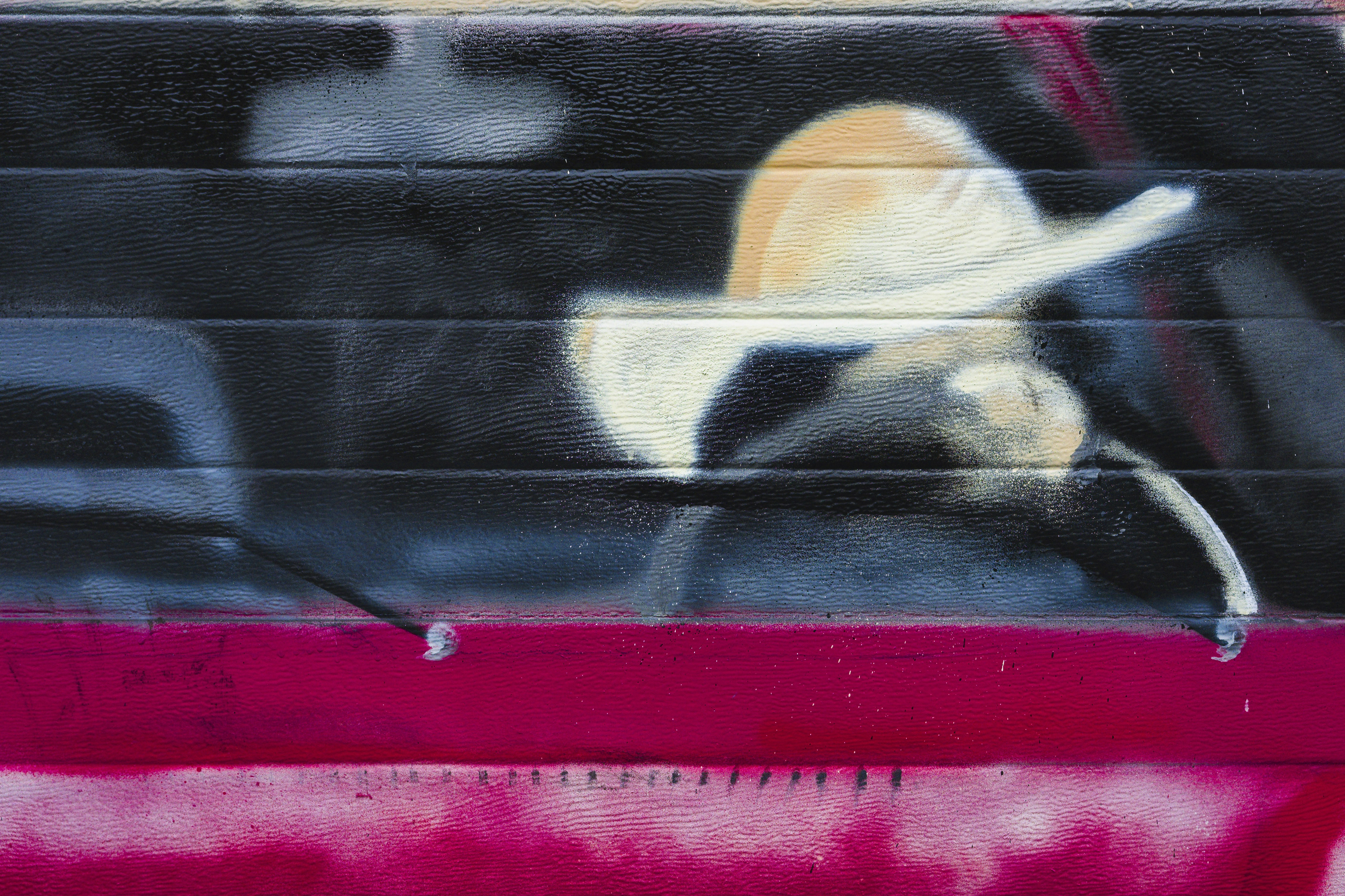 Straw-Hatted Moment: A Cream Silhouette Across a Magenta Graffiti Strip