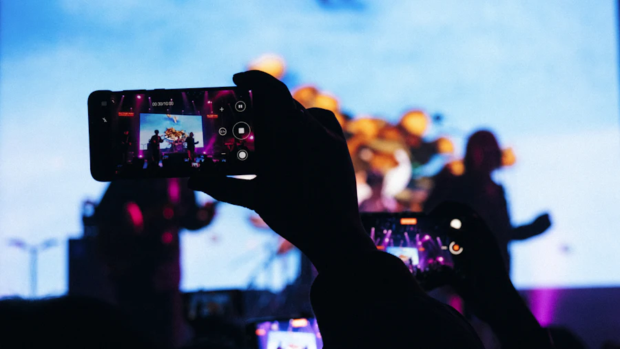 Silhouetted hands hold up smartphones recording a live concert, with bright stage lights and blurred performers in the background.