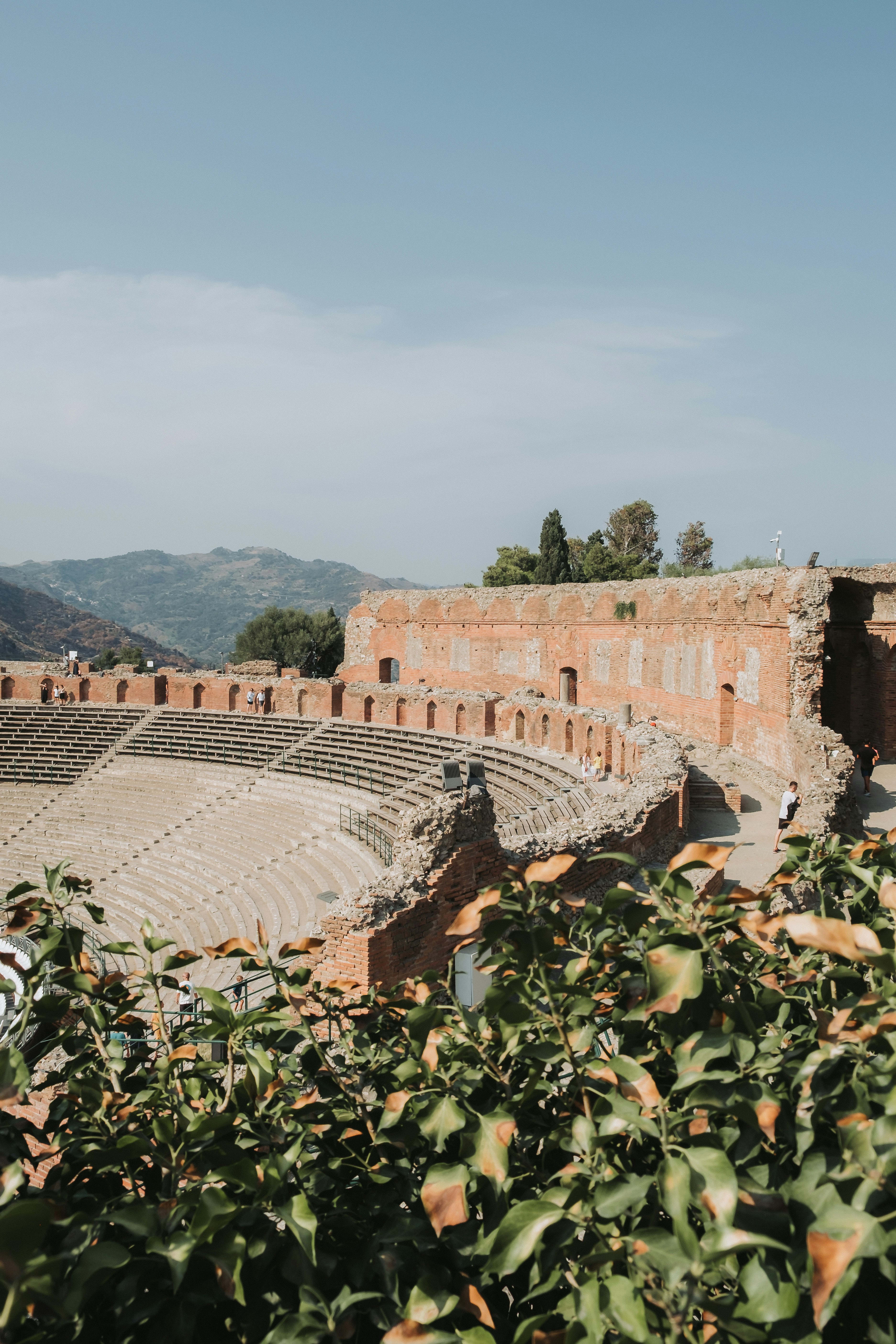 Ruins of an ancient amphitheater surrounded by lush greenery under a clear blue sky.