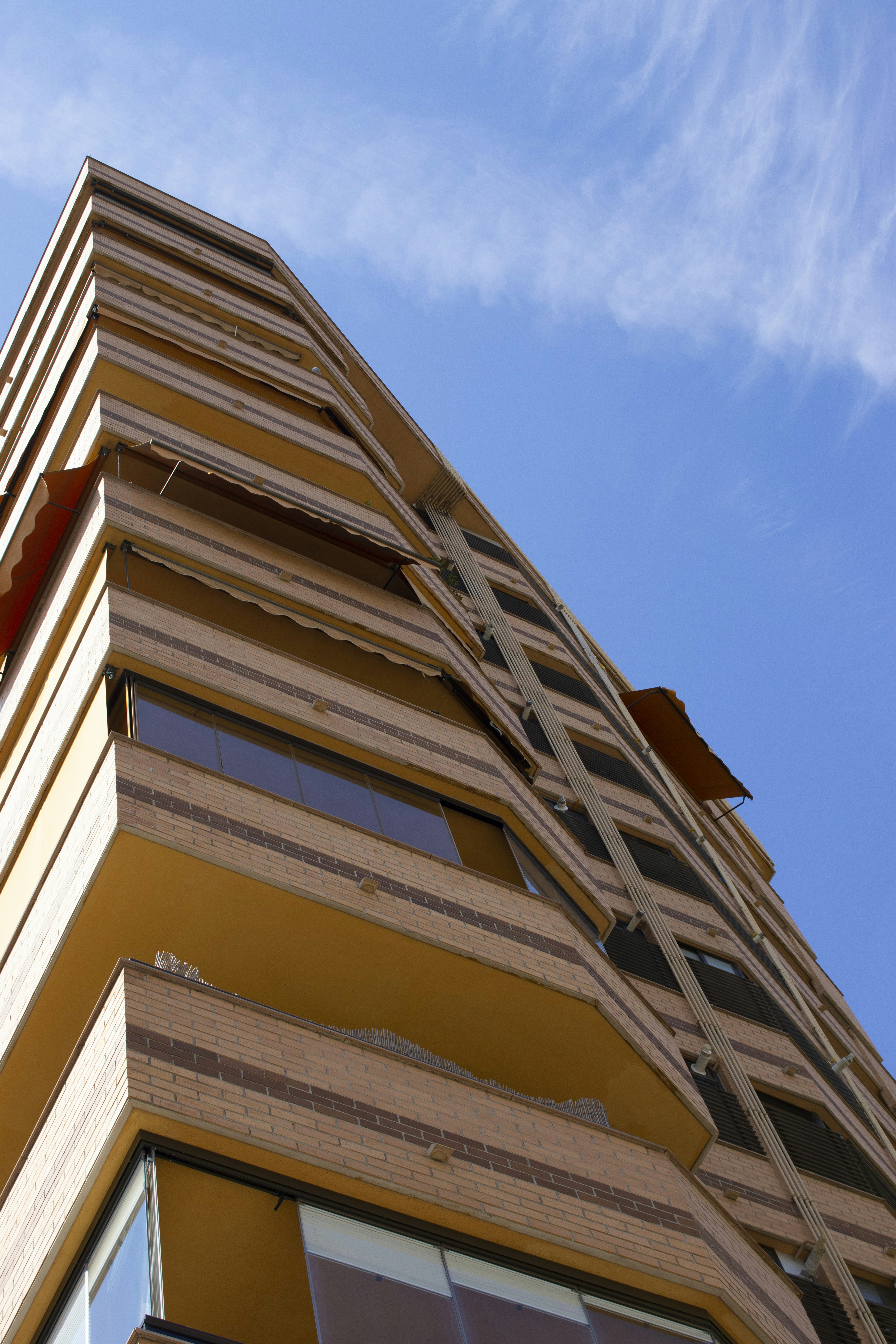 A towering building captured from a low angle, showcasing its unique facade and balconies against a clear blue sky.