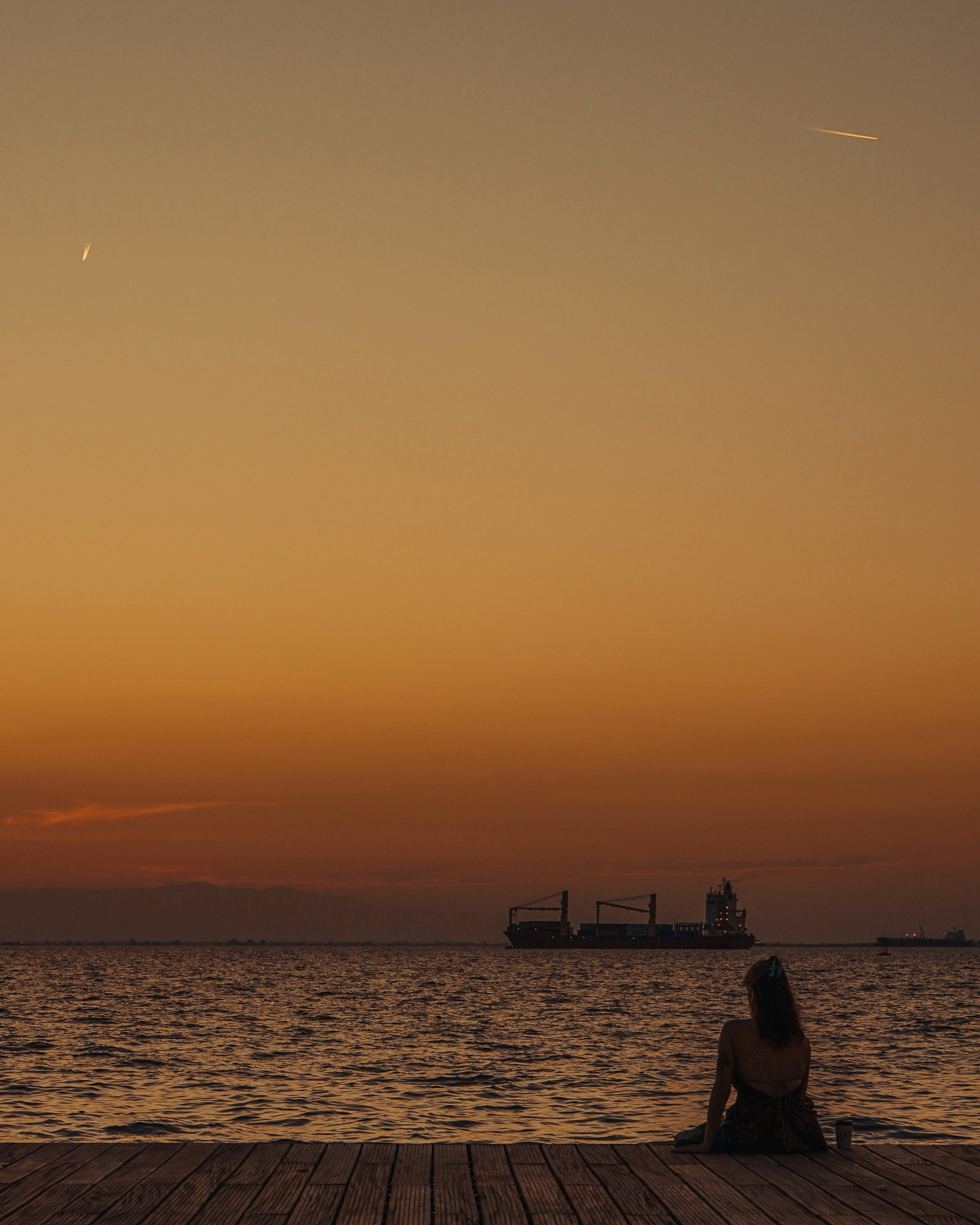A woman sitting on a dock watching the sunset photo – Free Sunset Image ...