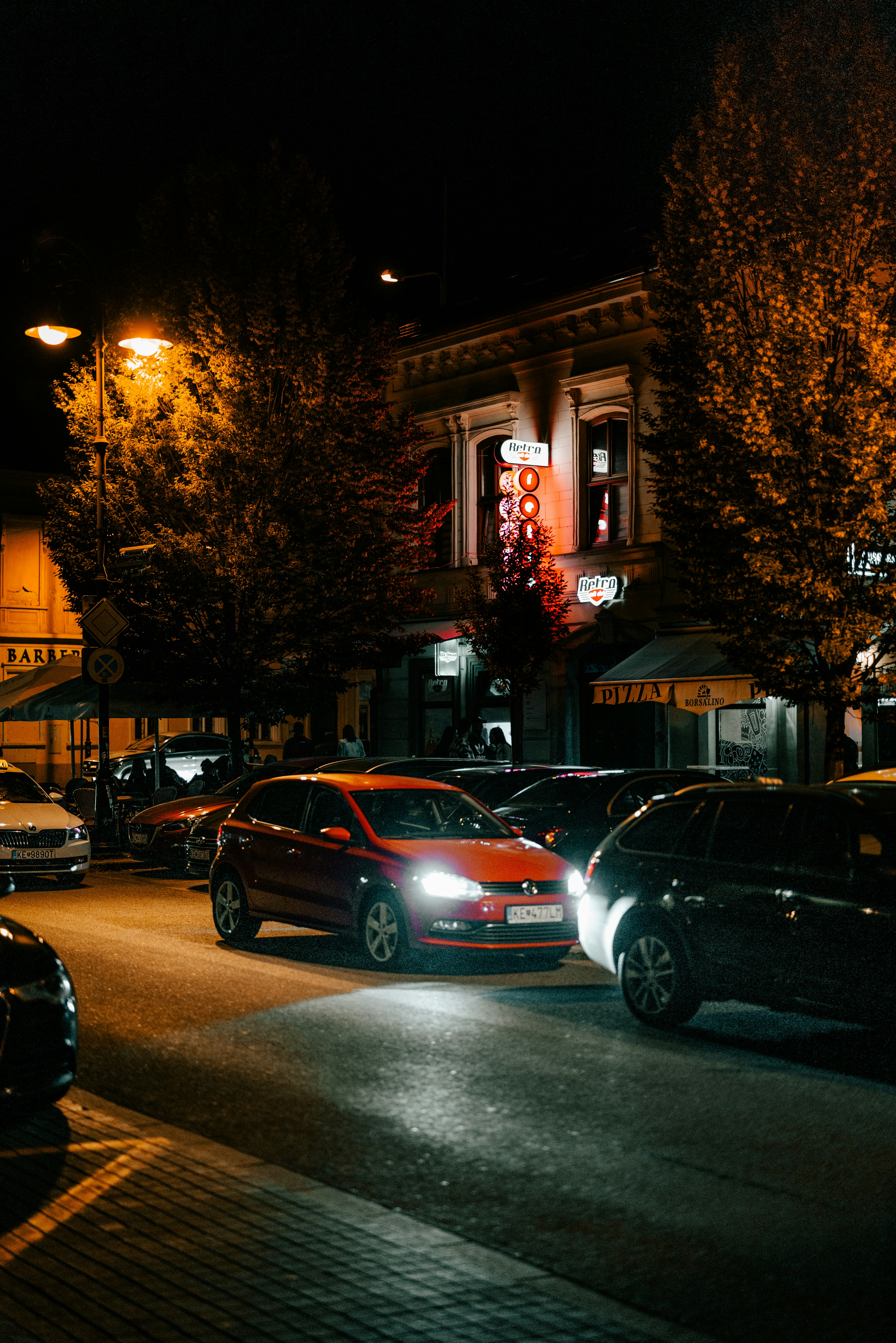 Nighttime city street in Košice with cars and illuminated shop signs.