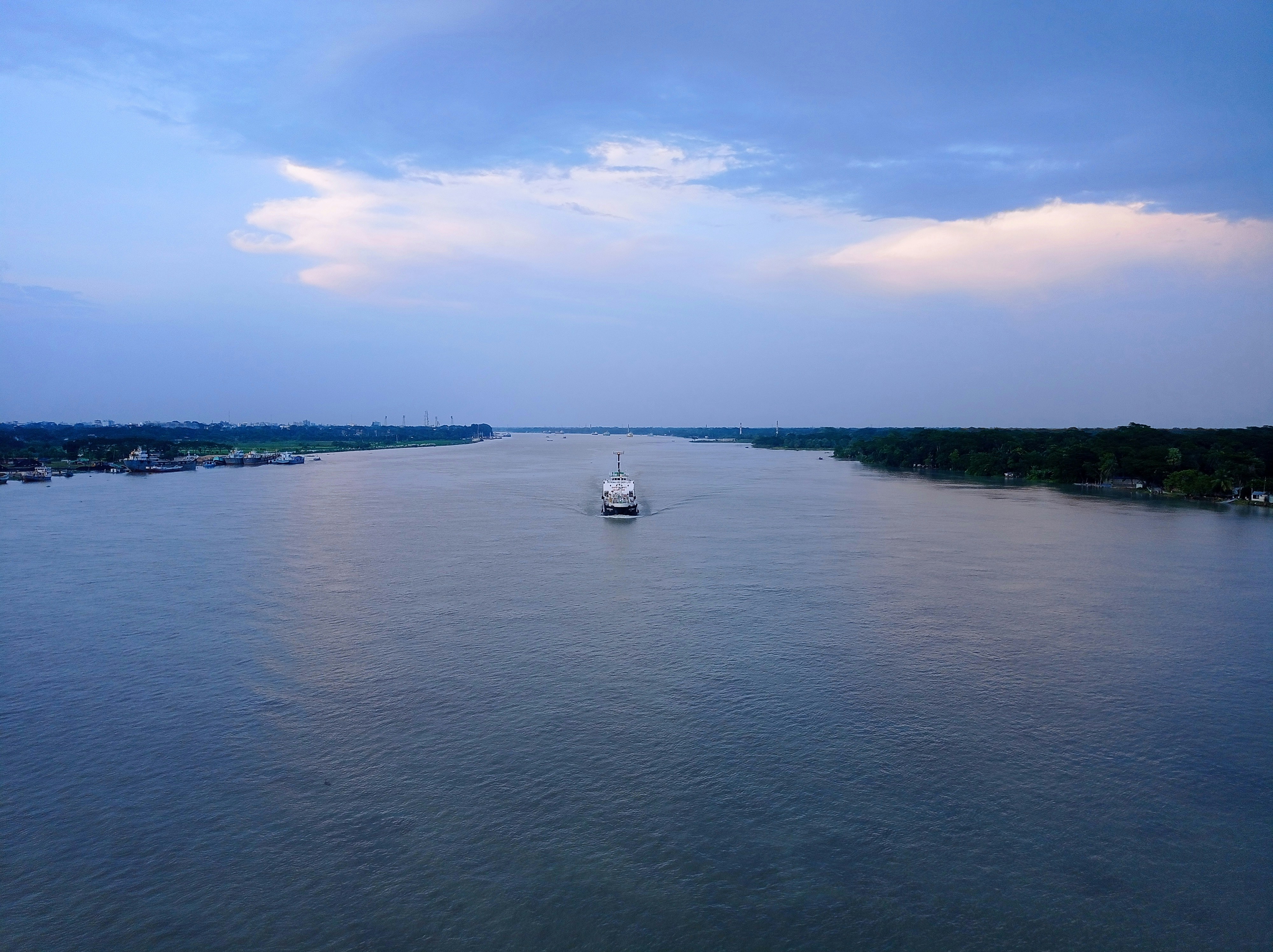 Wide river with a lone boat under a serene, cloudy sky at dusk.