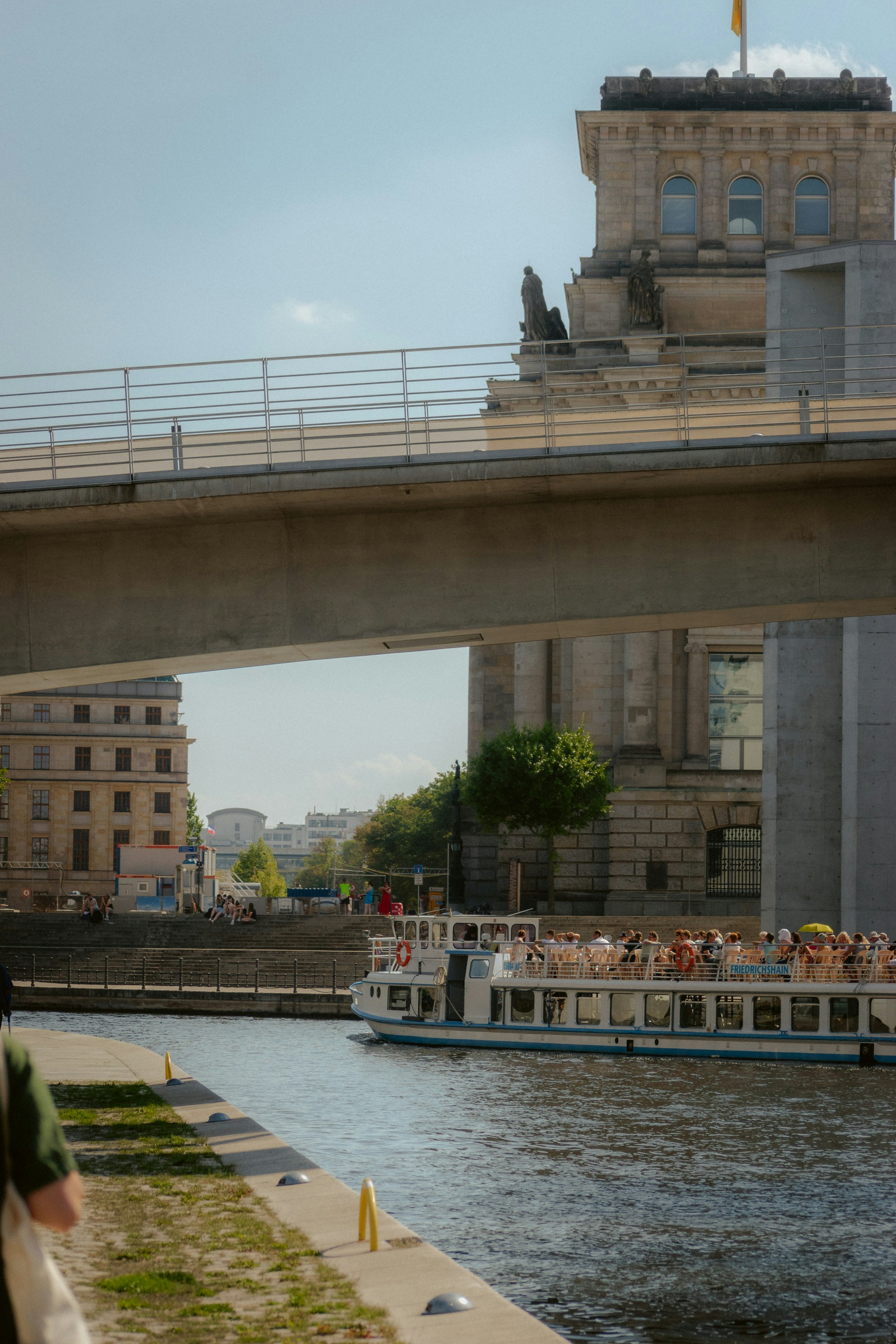 Sunlit Tour Boat Under a Monumental City Bridge