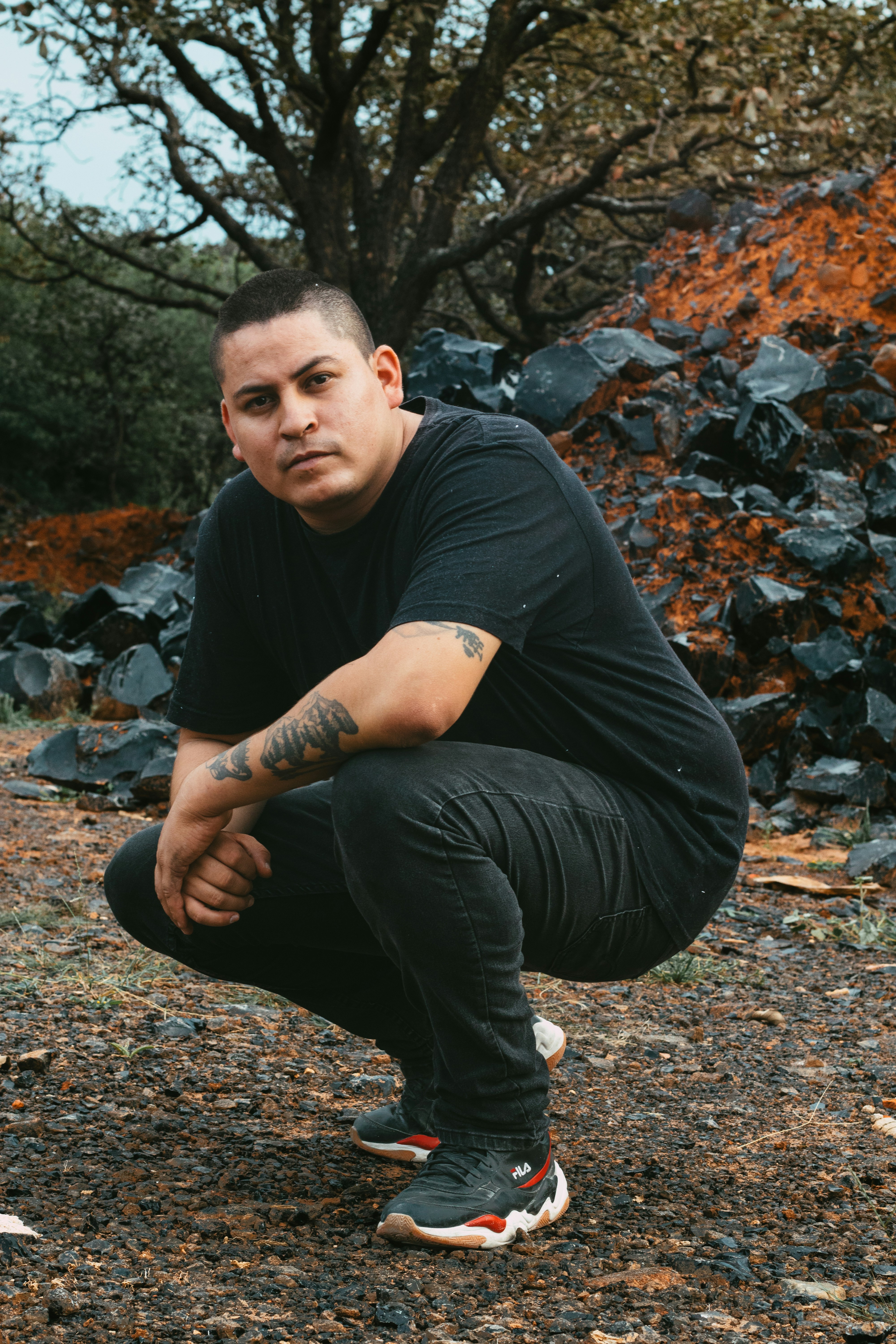 A man squatting on the ground with a tree in the background photo ...