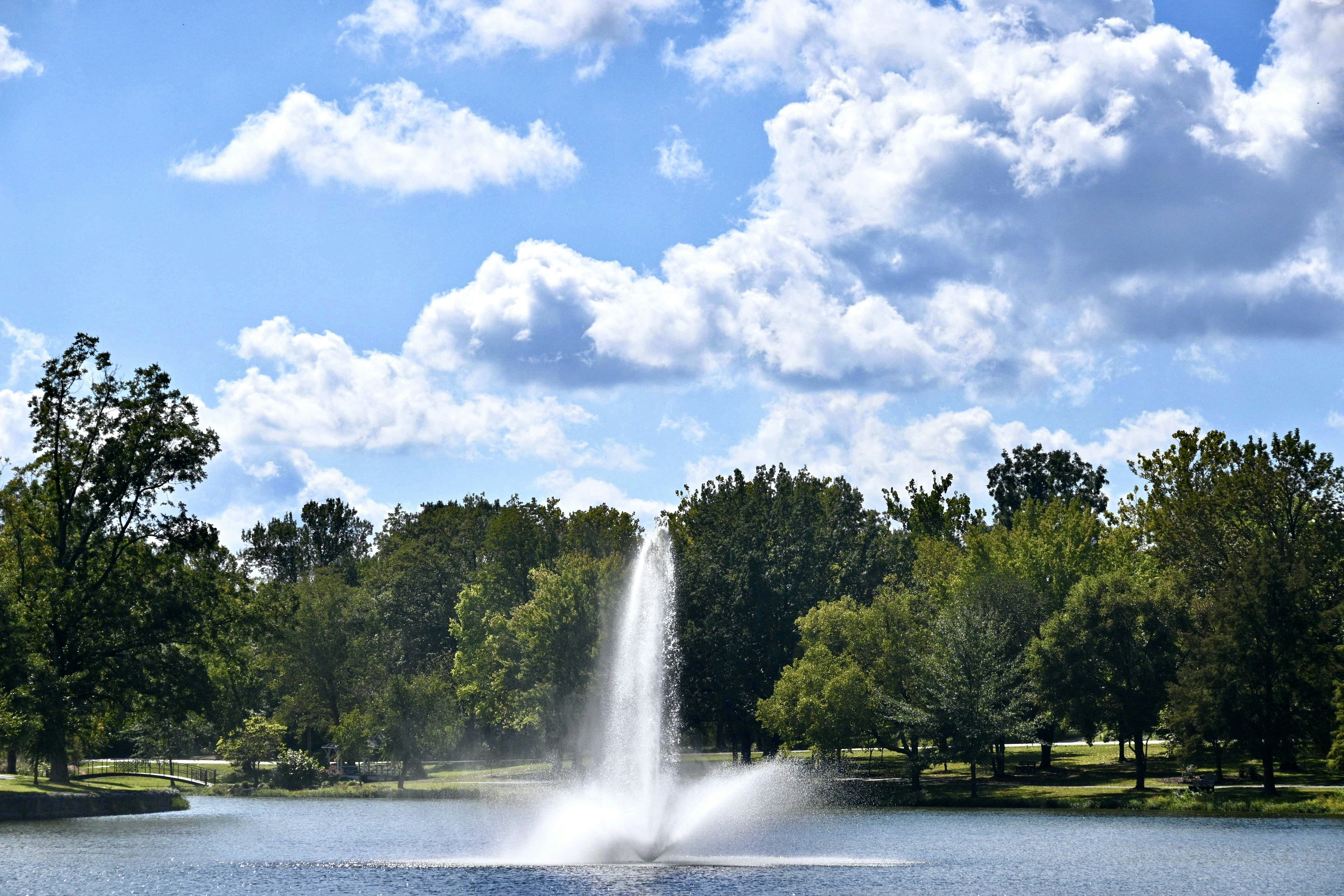 A large fountain spewing water into a lake surrounded by trees photo ...