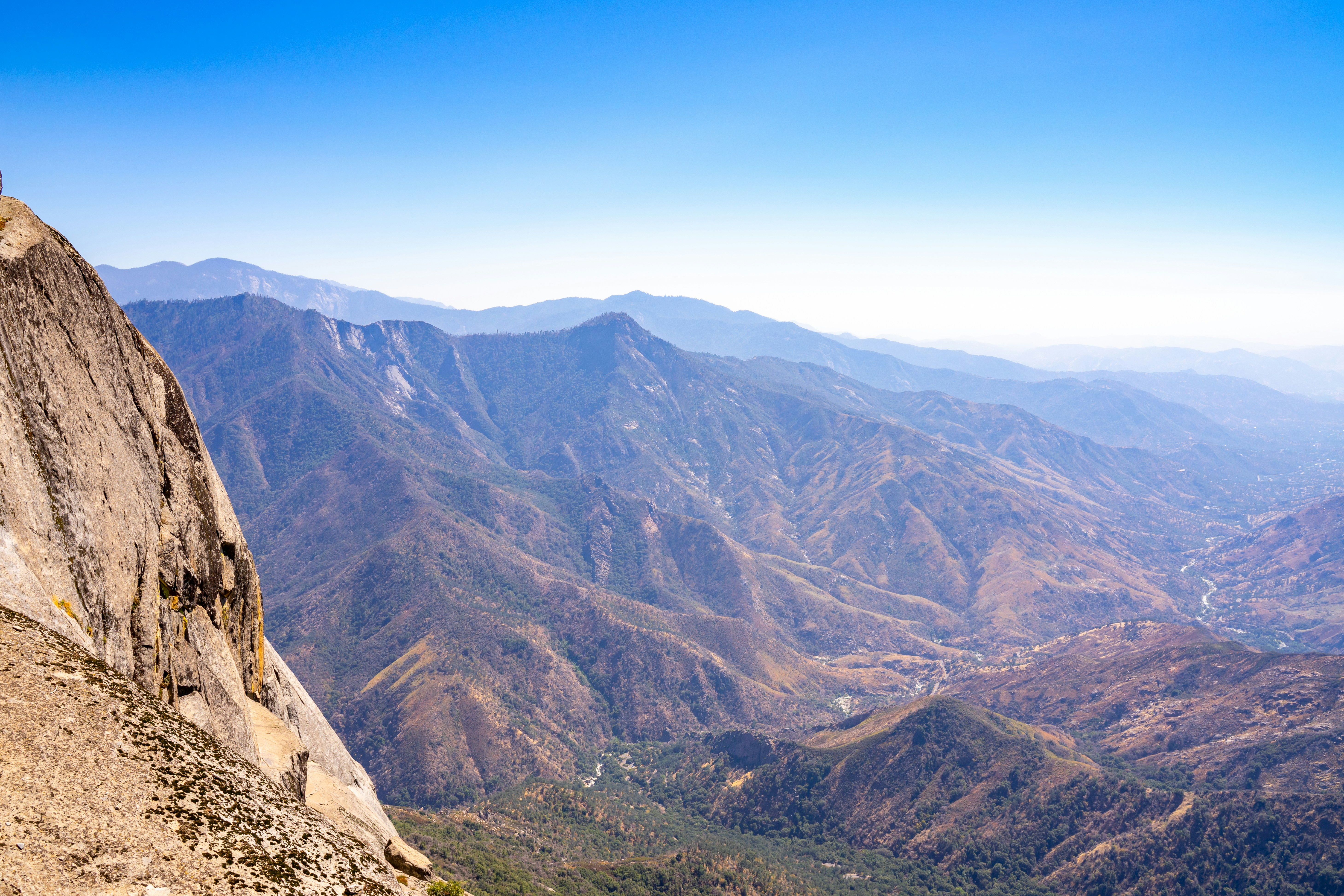 Sunlit mountain range with rugged terrain under a clear blue sky.