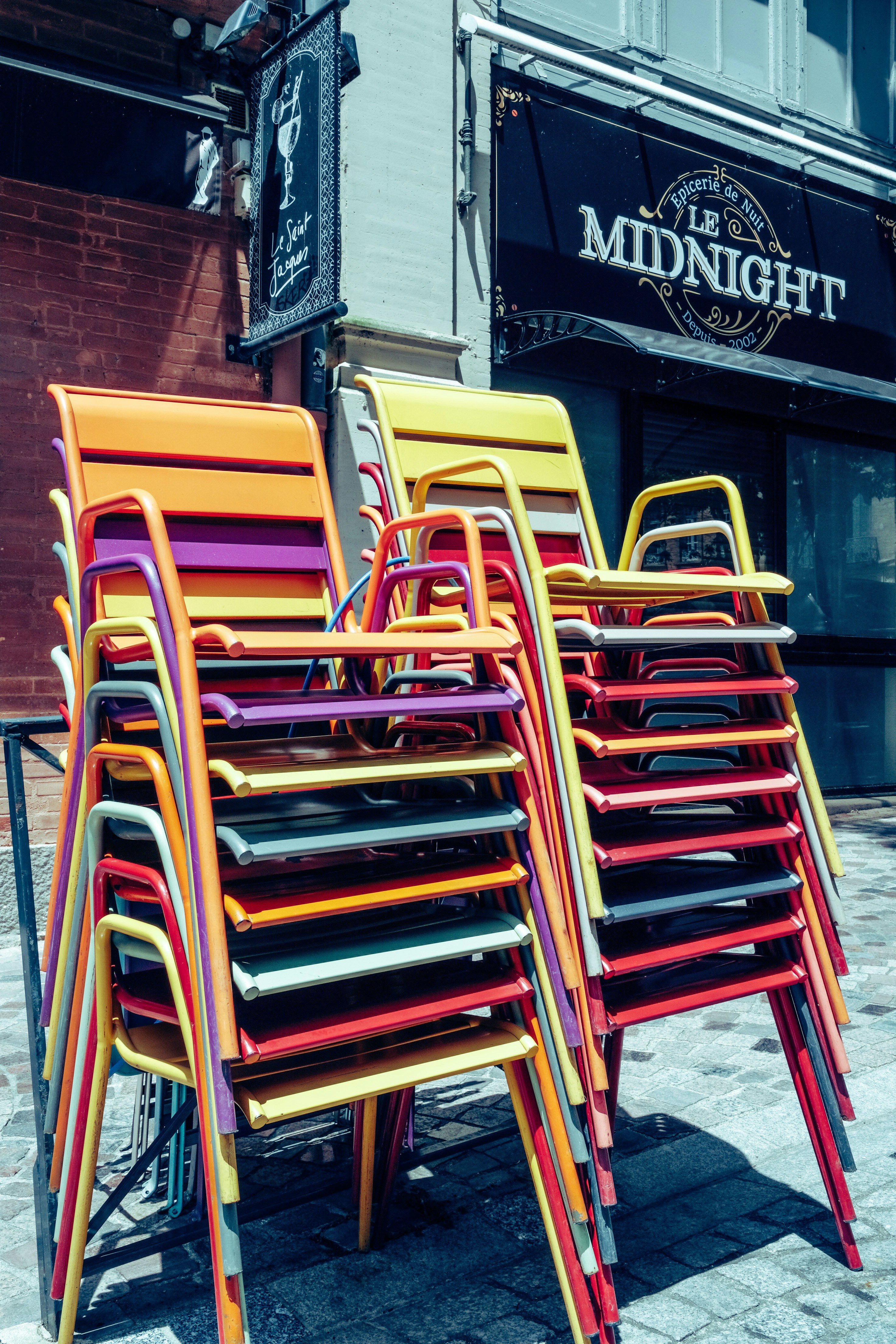 Rainbow Stack: Colorful Chairs Piled Outside Le Midnight Café