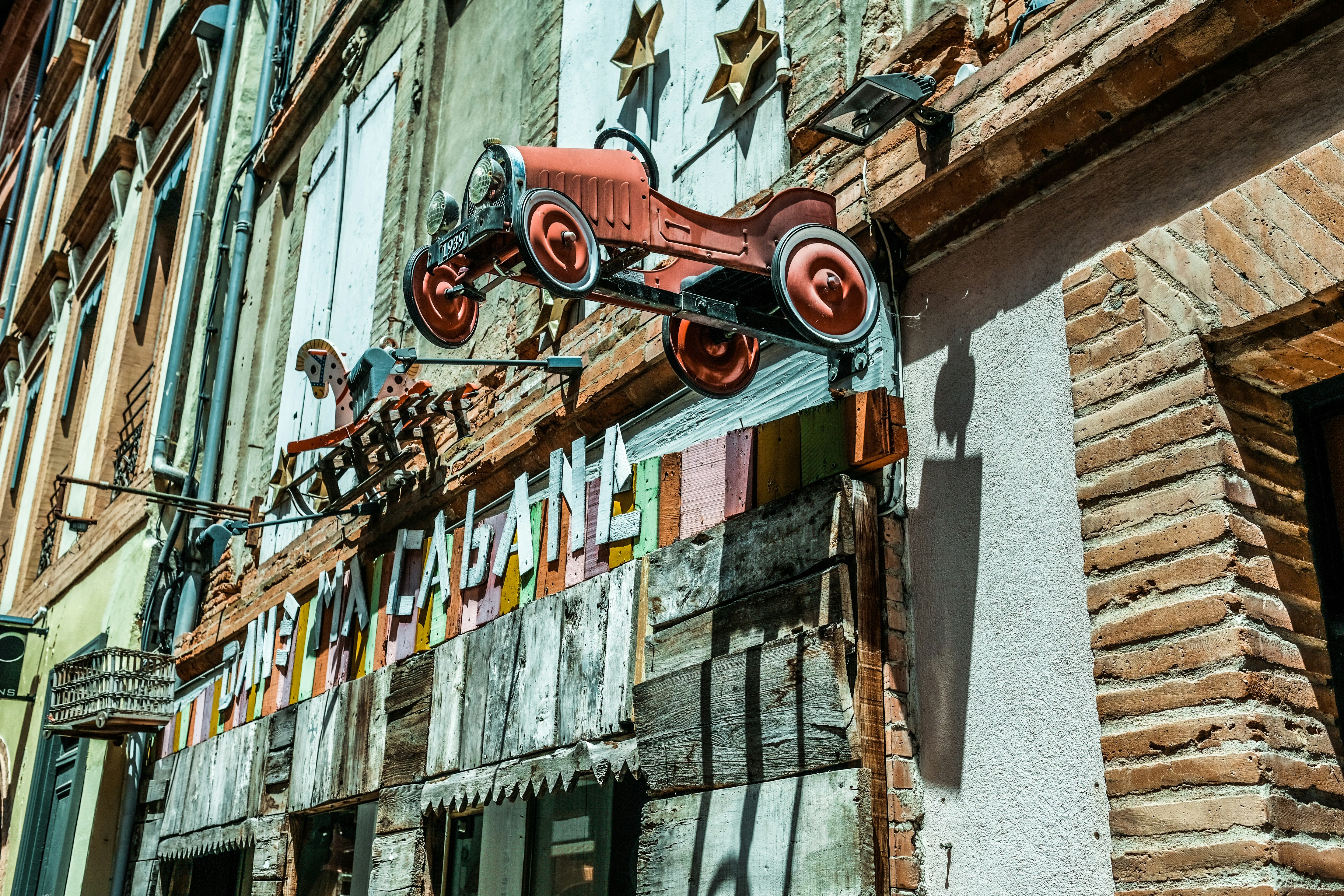 Vintage red car and bicycle mounted on a colorful building facade with brick and wooden accents.