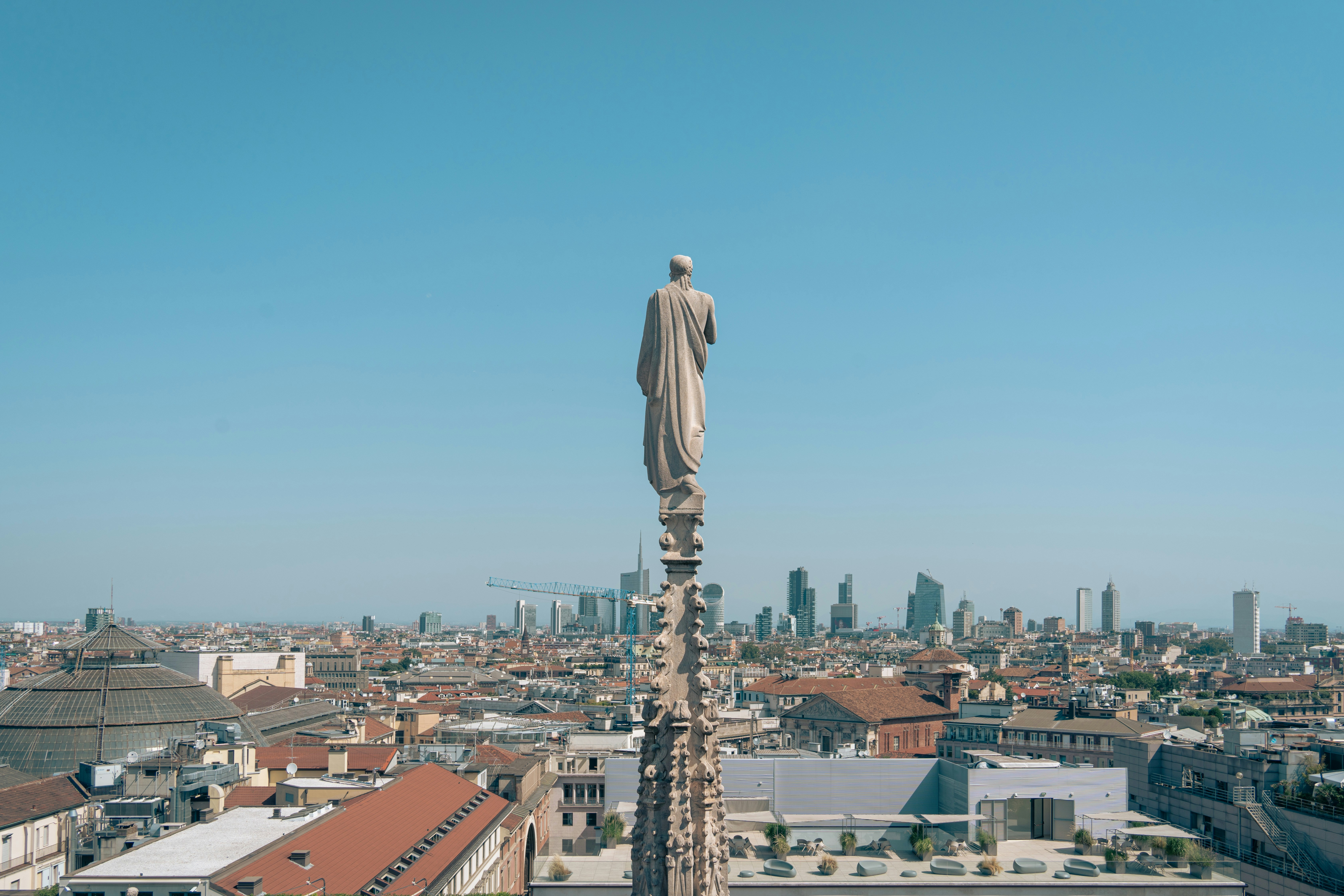 Skyward Sentinel over a Cityscape: A statue crowns a sculpted column above red rooftops.