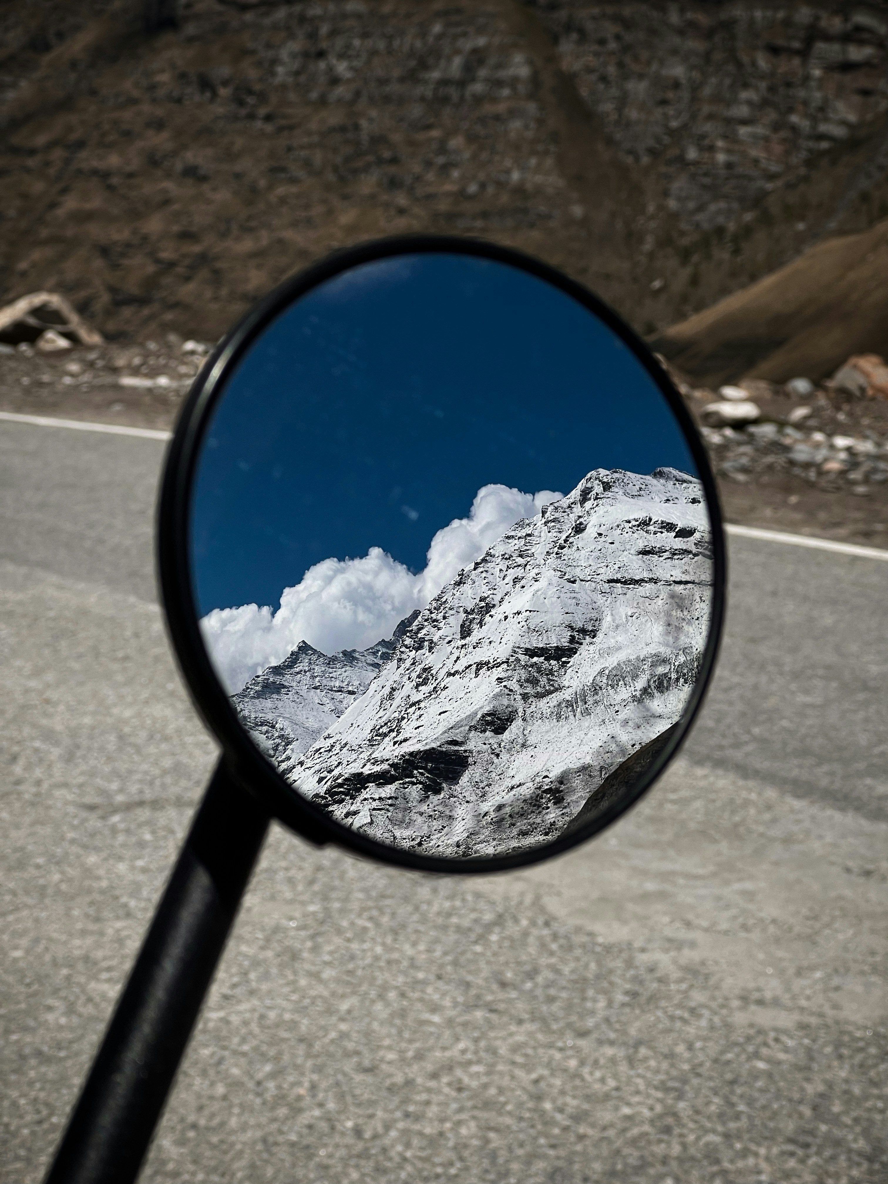 White mountains of Lahaul Valley reflected in a rearview mirror by the roadside.