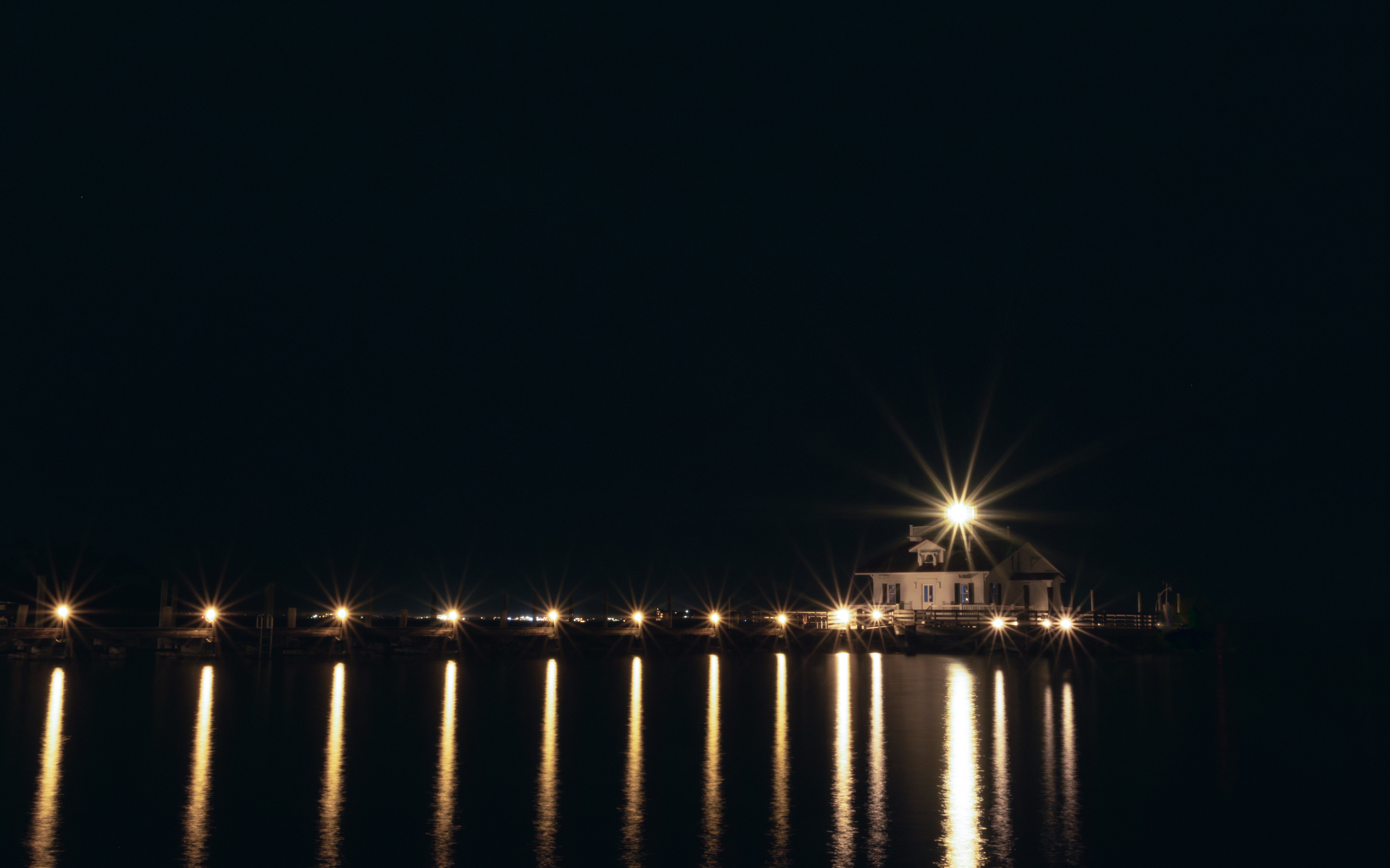 A lighthouse is lit up at night on the water photo – Free Night Image ...