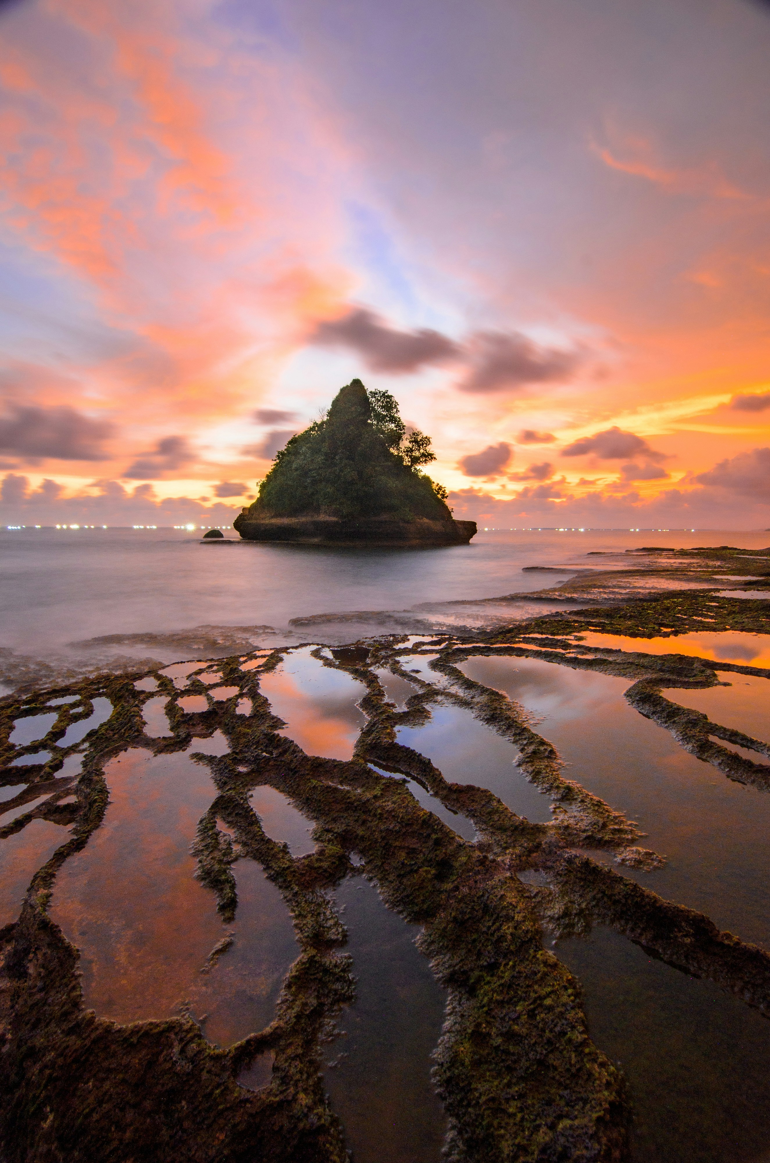 Last Light Island: a tree-topped isle framed by a tidal sculpture at sunset