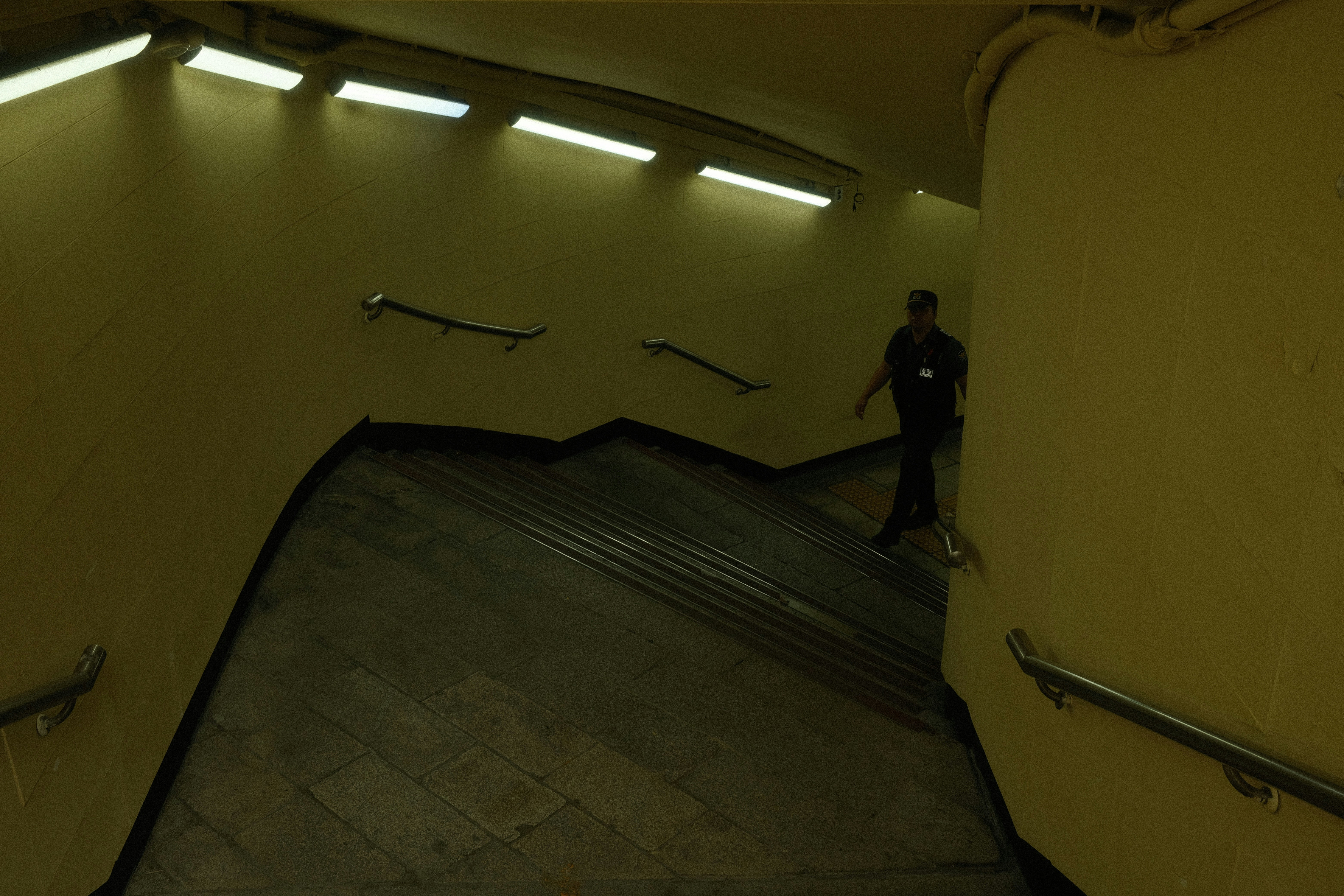 Lone Figure Descends a Yellow-Glow Underground Stairwell