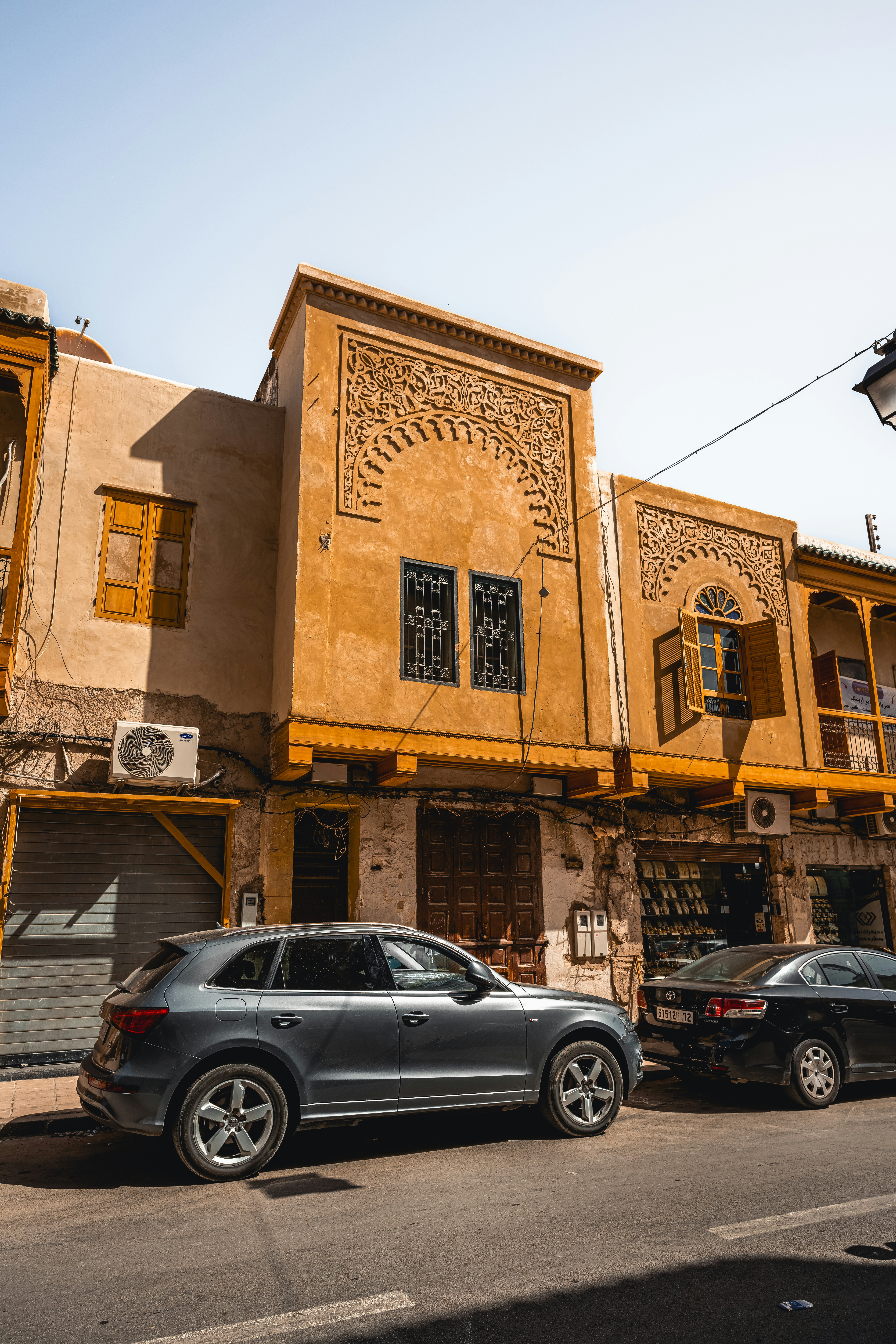 Sunlit Adobe Facade: A Street Scene with Parked Cars and Ornate Archways