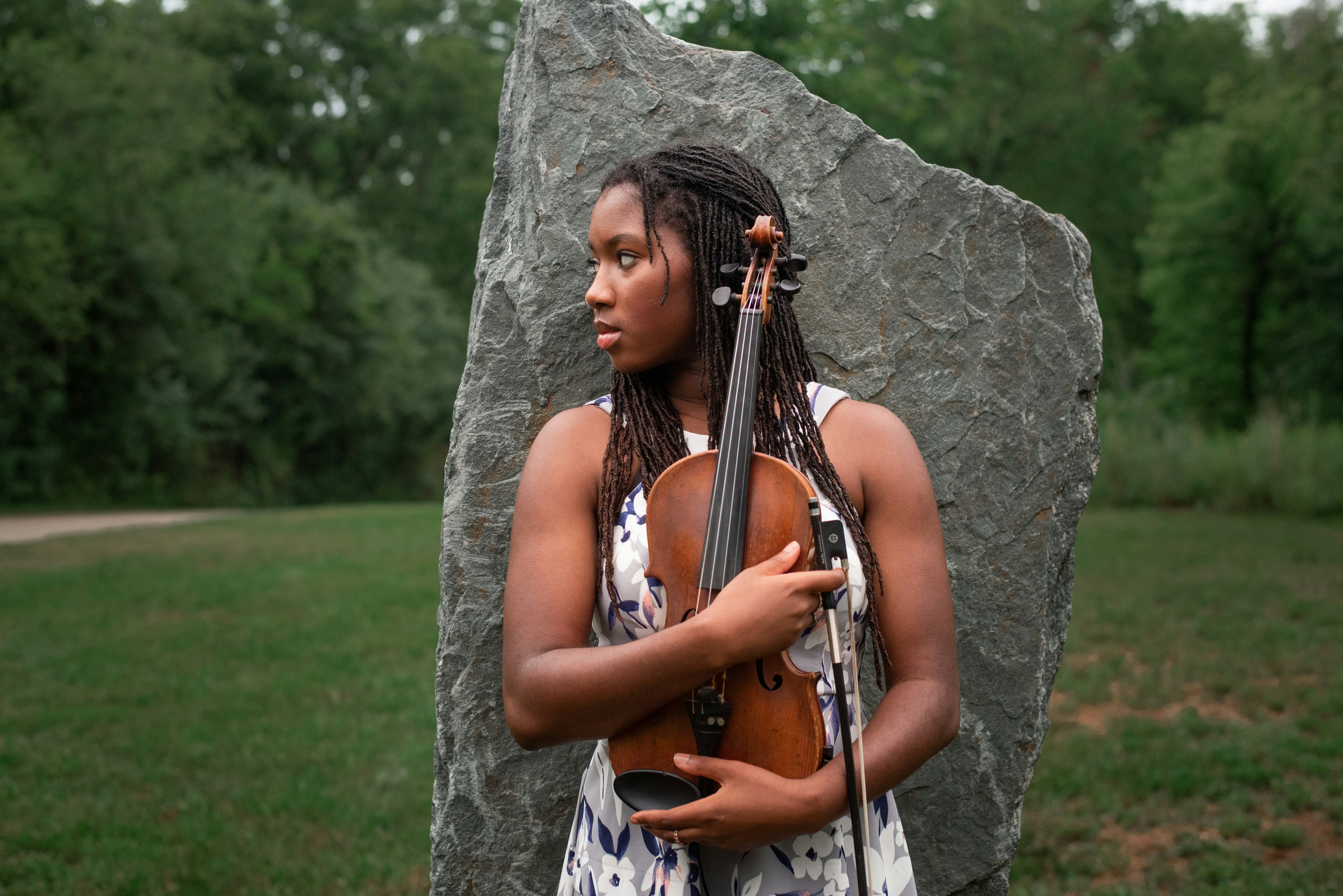 A woman with dreadlocks holding a violin in front of a rock photo ...