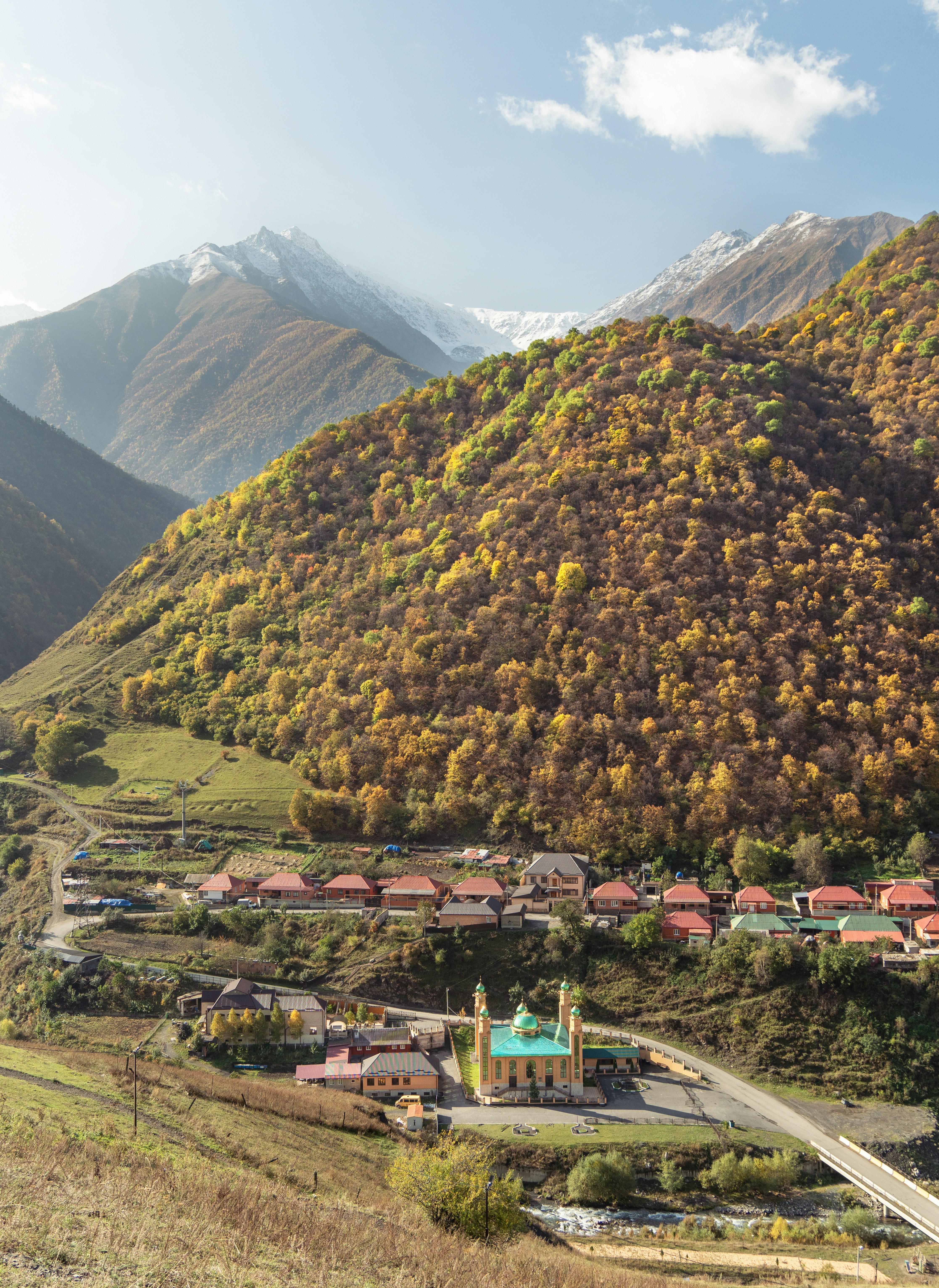 Turquoise-domed mosque at the valley's edge under autumn-tinted peaks