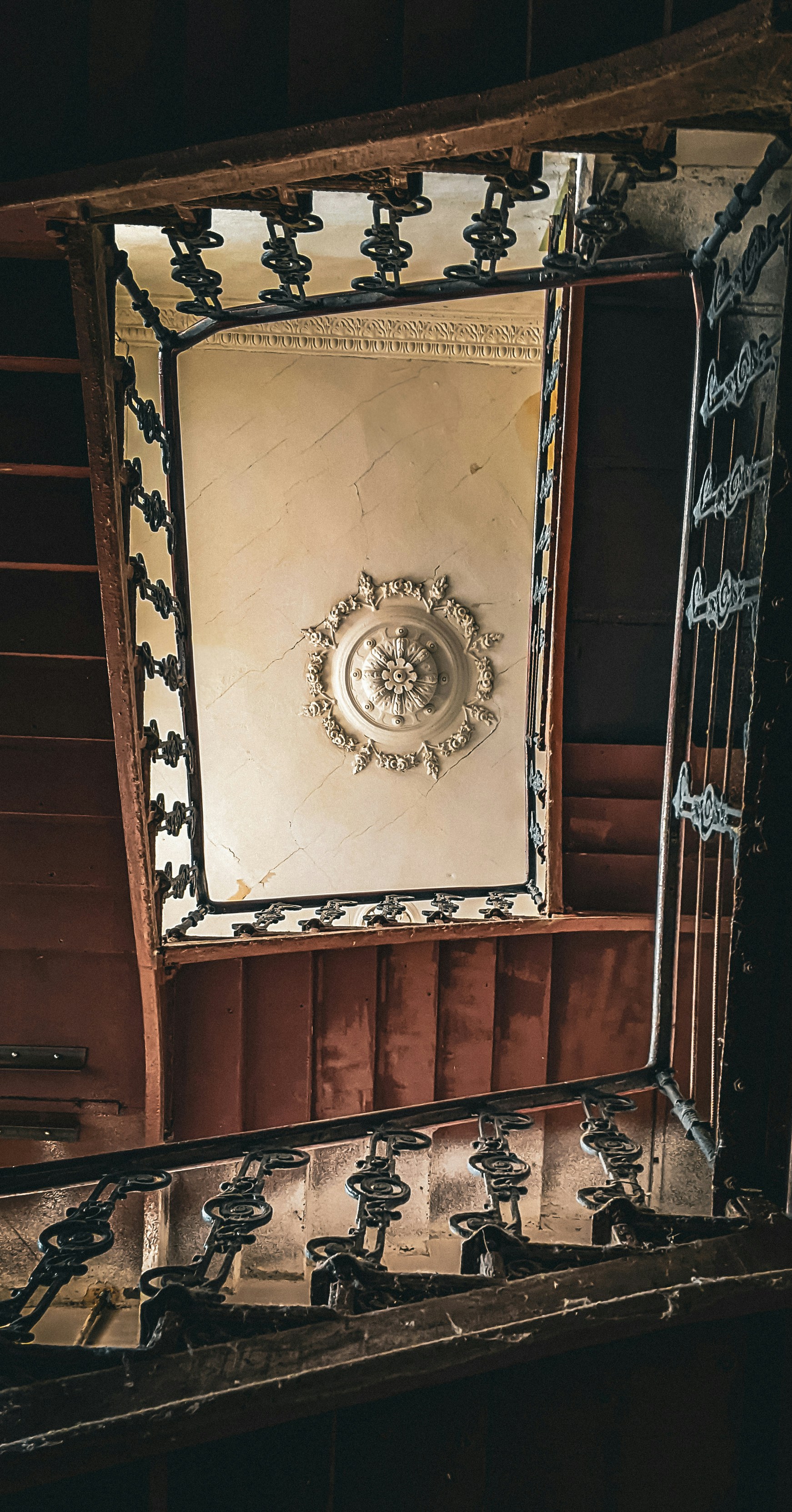 A photograph taken from the base of a spiraling staircase reveals a central ornamental ceiling medallion framed by wrought-iron railings.