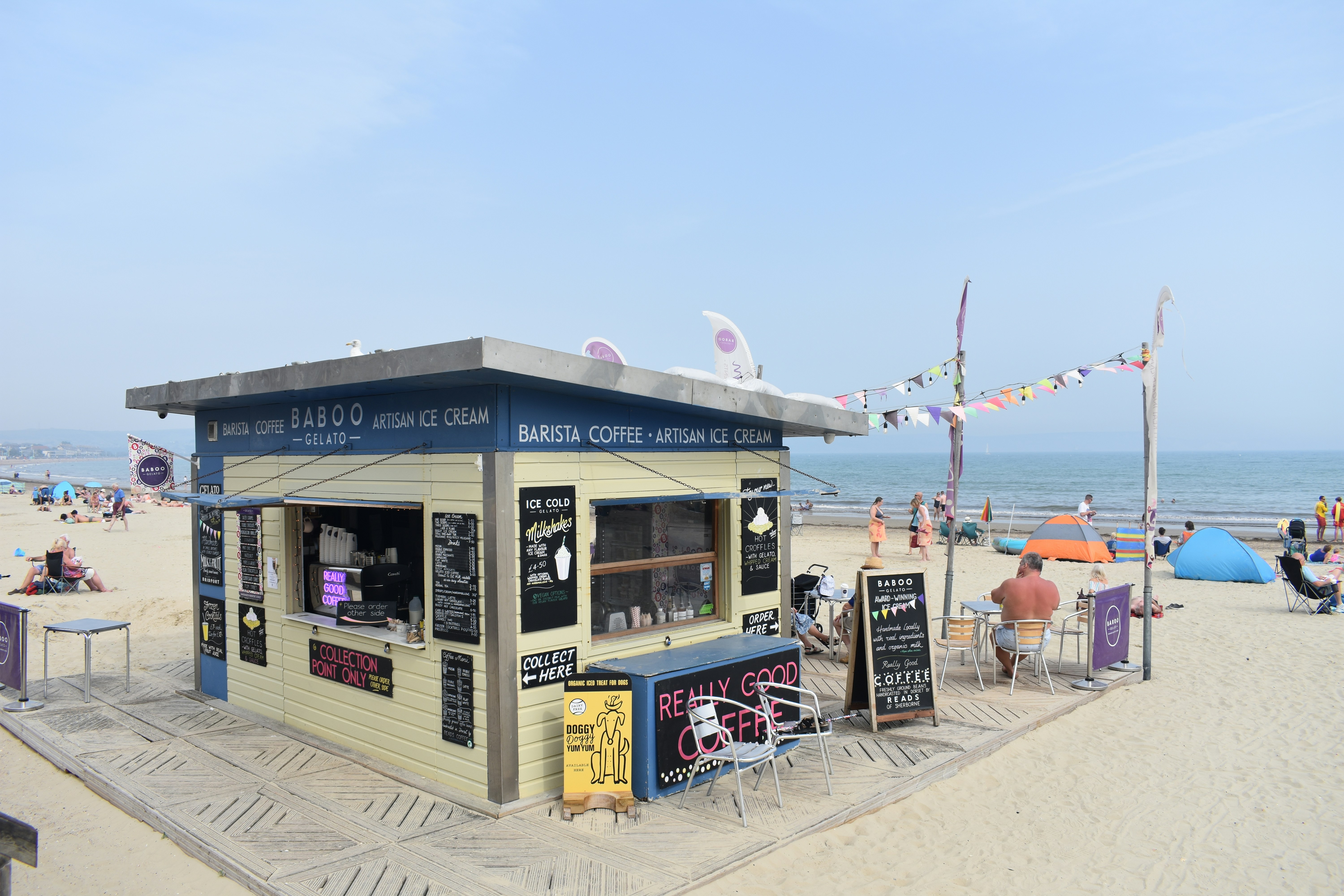 A vibrant beachside kiosk offering artisan ice cream and coffee, surrounded by sunbathers and colorful beach umbrellas.