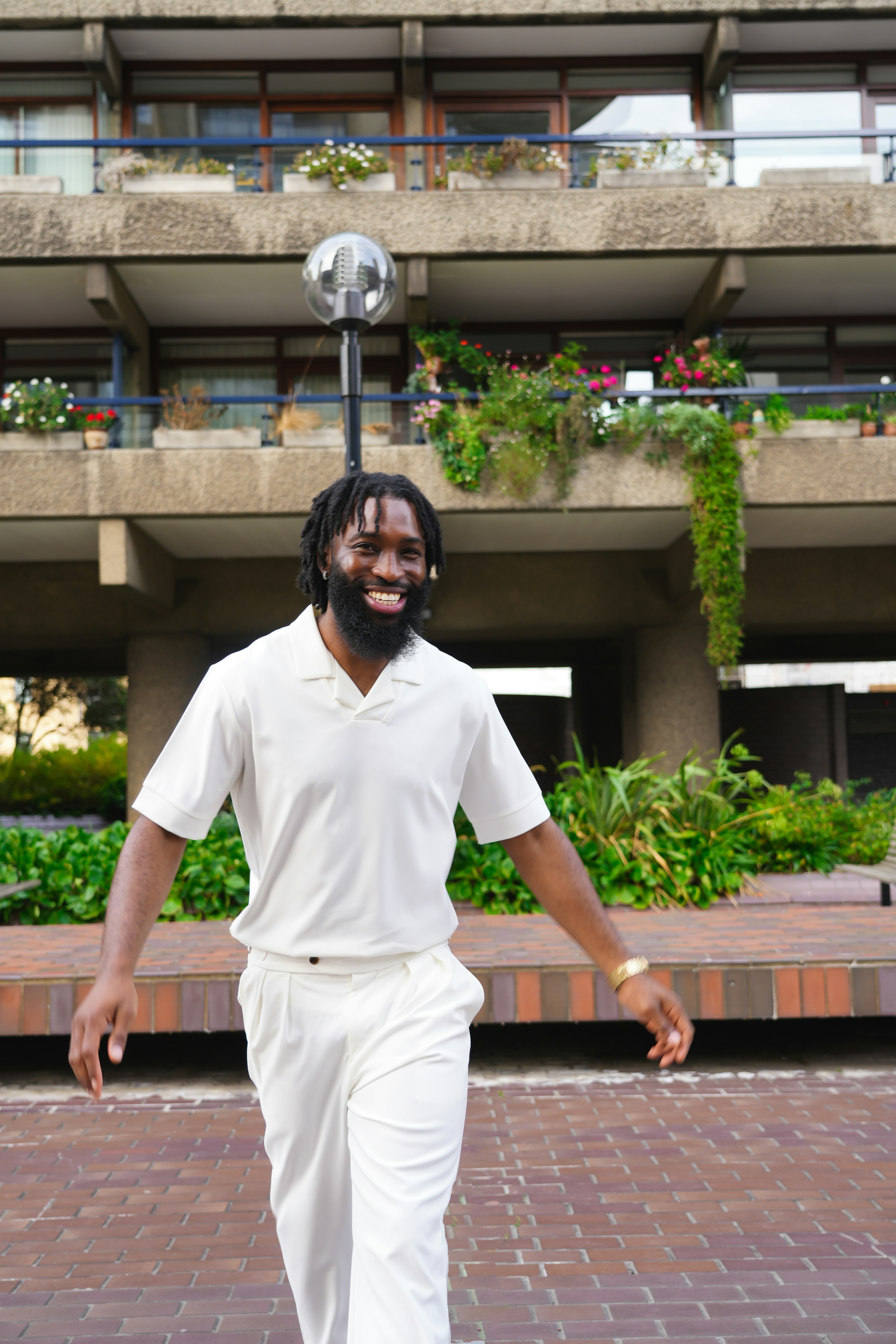 Sunlit stride: a man in white amid planter-filled balconies in a modern courtyard