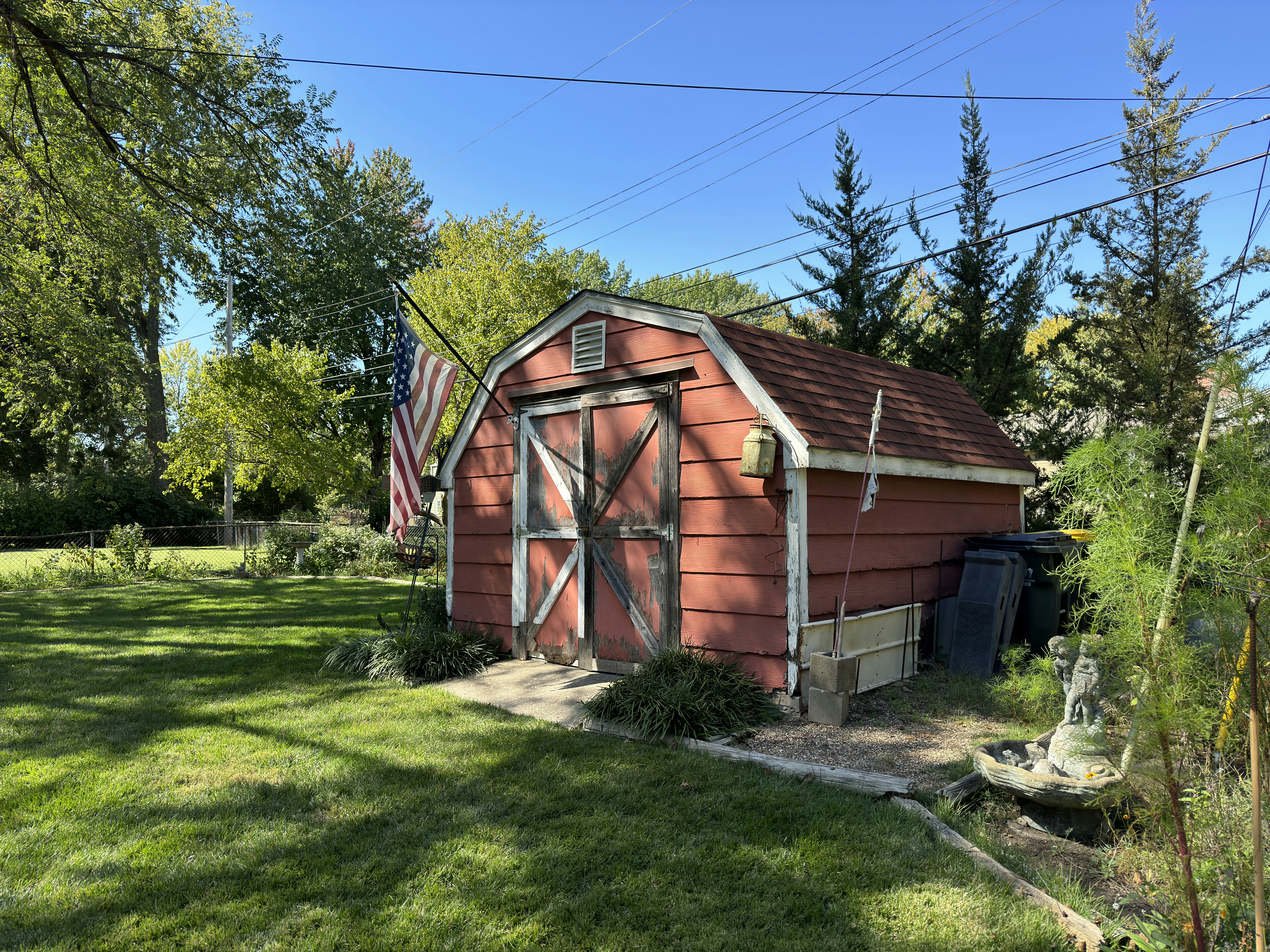 Red Shed Rendezvous: Flag, Garden Statue, and Morning Light