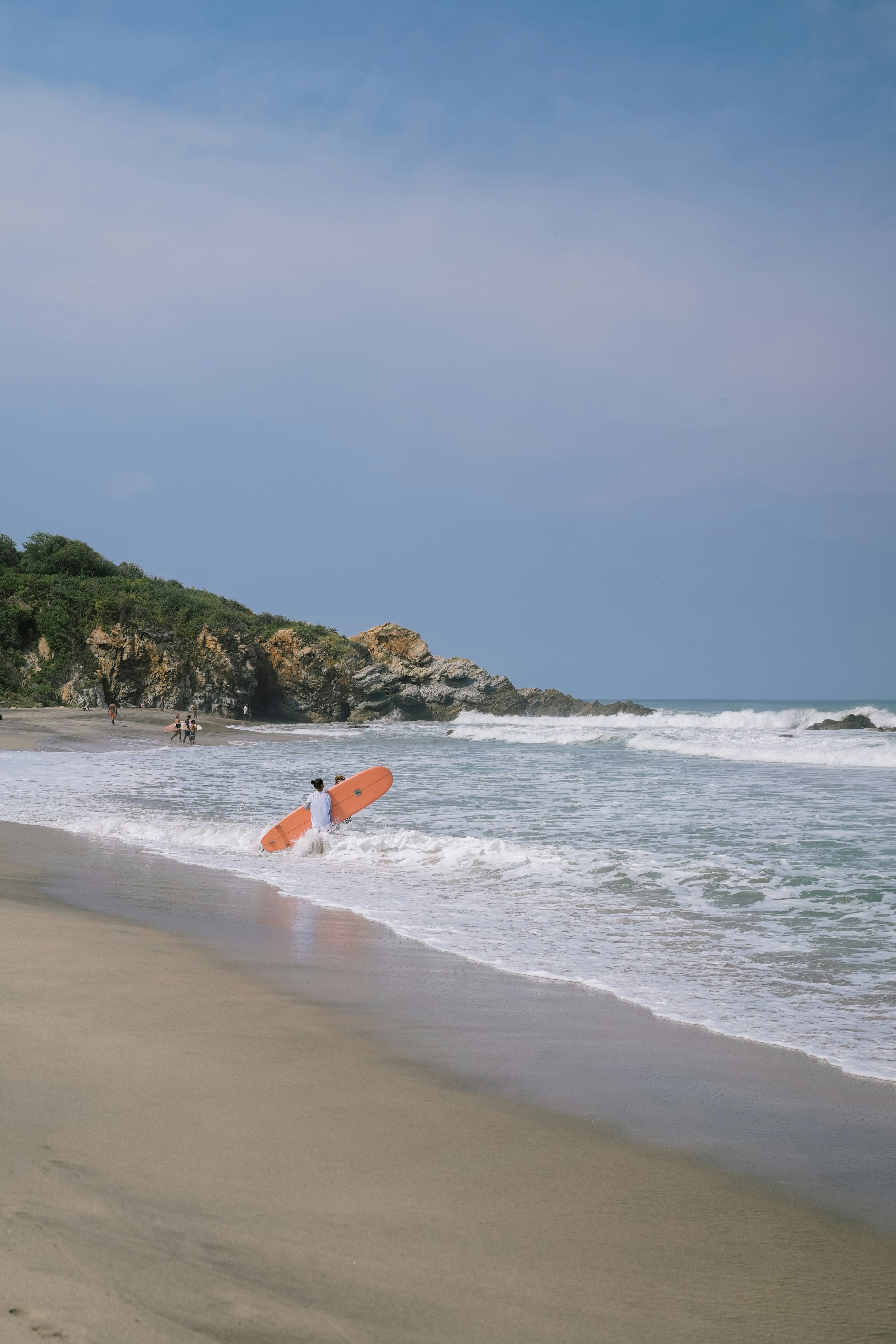 Surfer with Orange Board Approaches Gentle Shoreline near Rugged Rocks