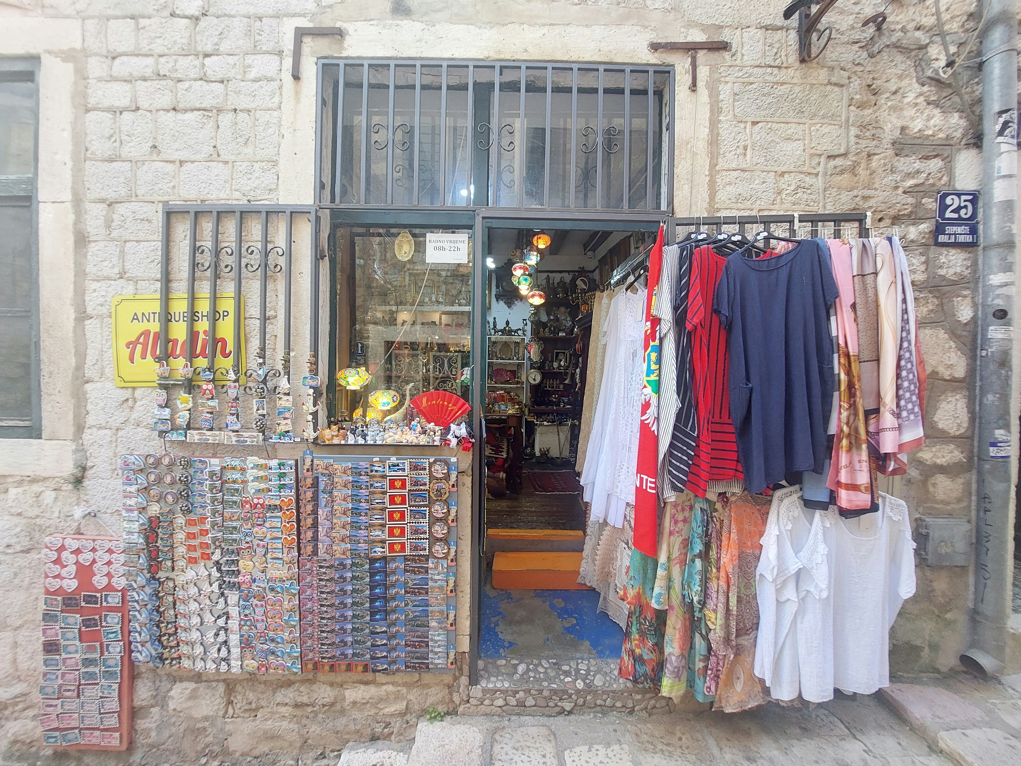 Small street shop displaying colorful clothing and souvenirs against a rustic stone wall.