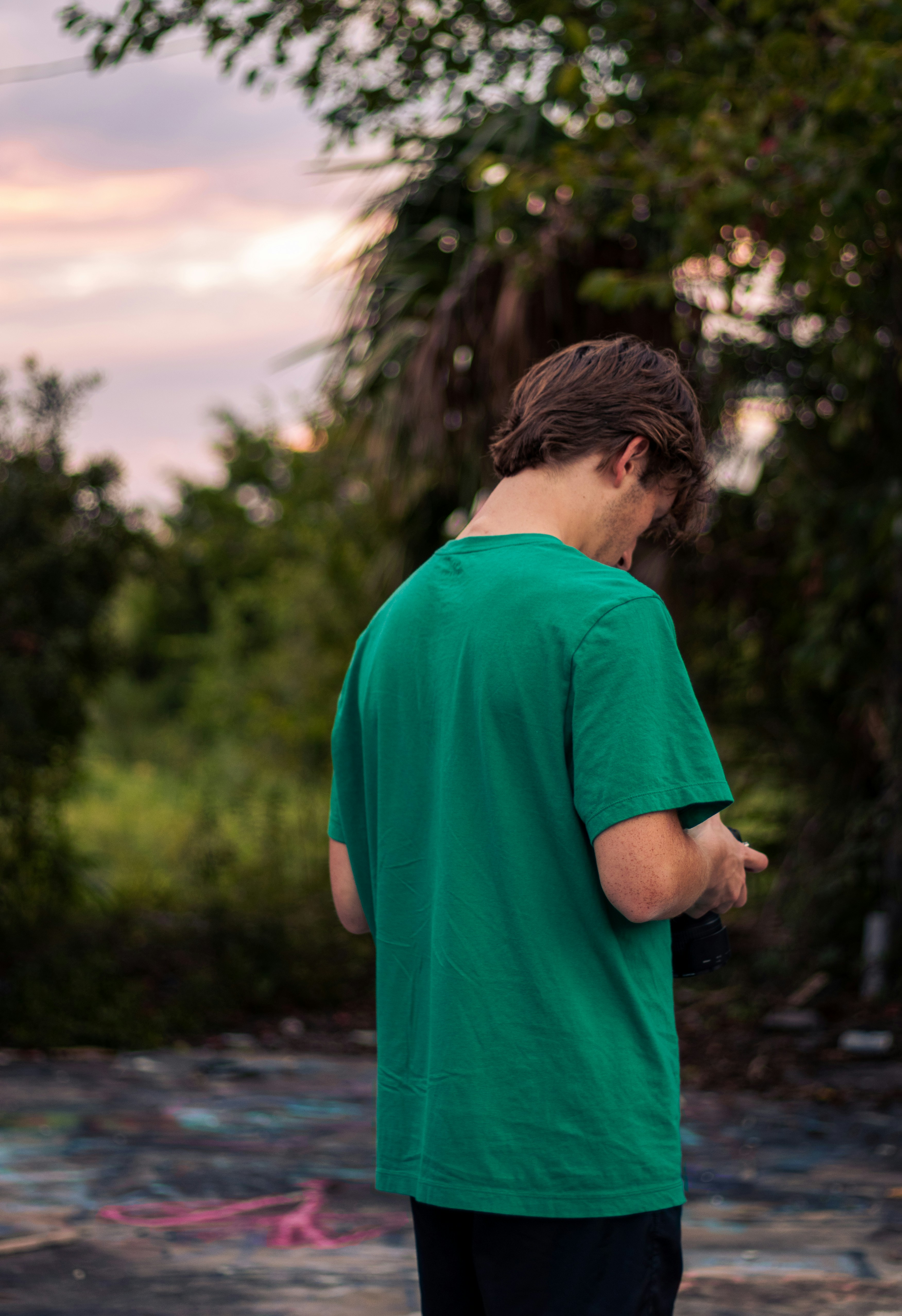 Dusk Portrait: Green-Tee Photographer Against a Graffiti-Lined Yard