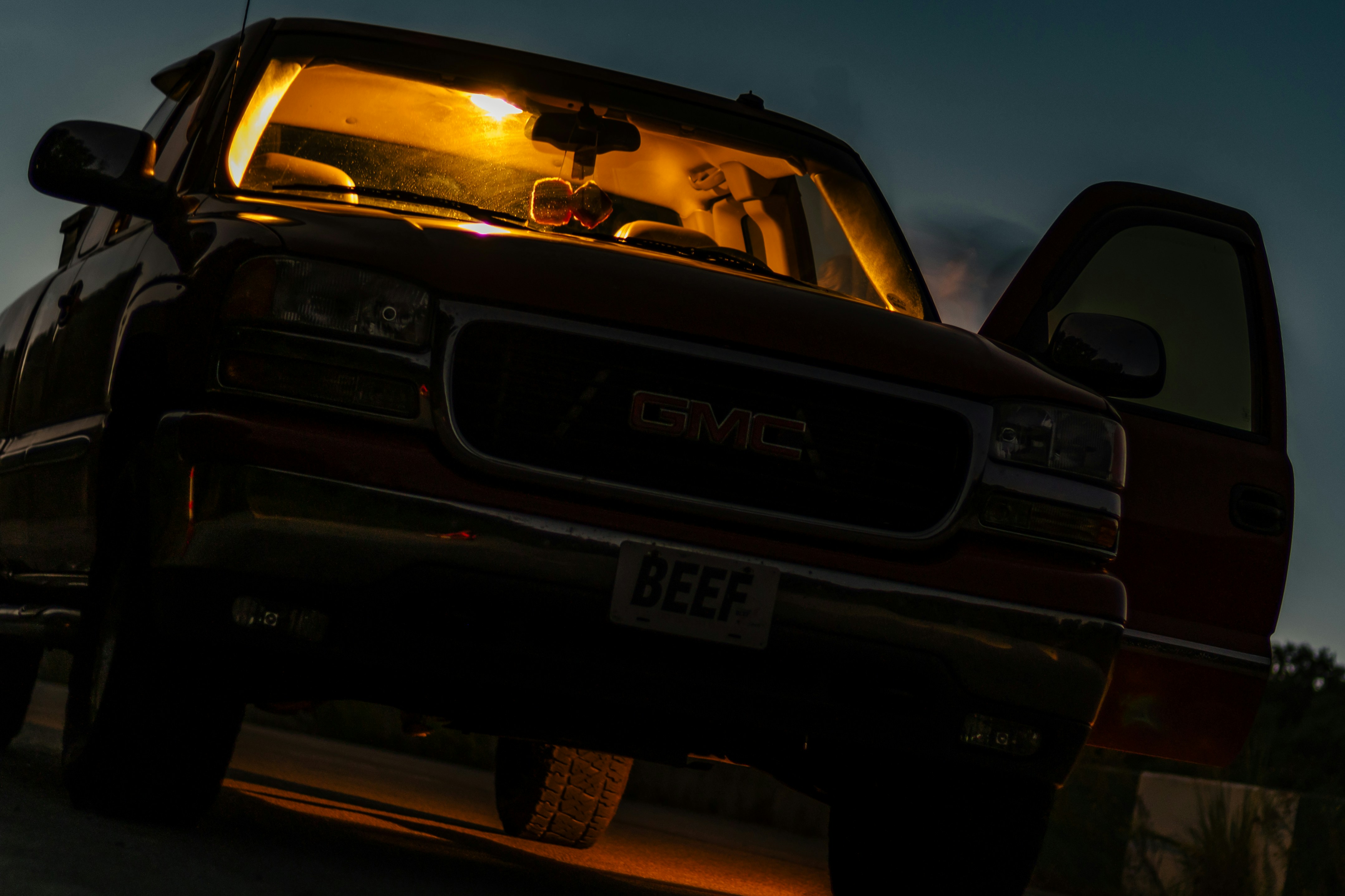 A GMC truck parked with its door ajar, illuminated by warm interior lights against a dusk backdrop.