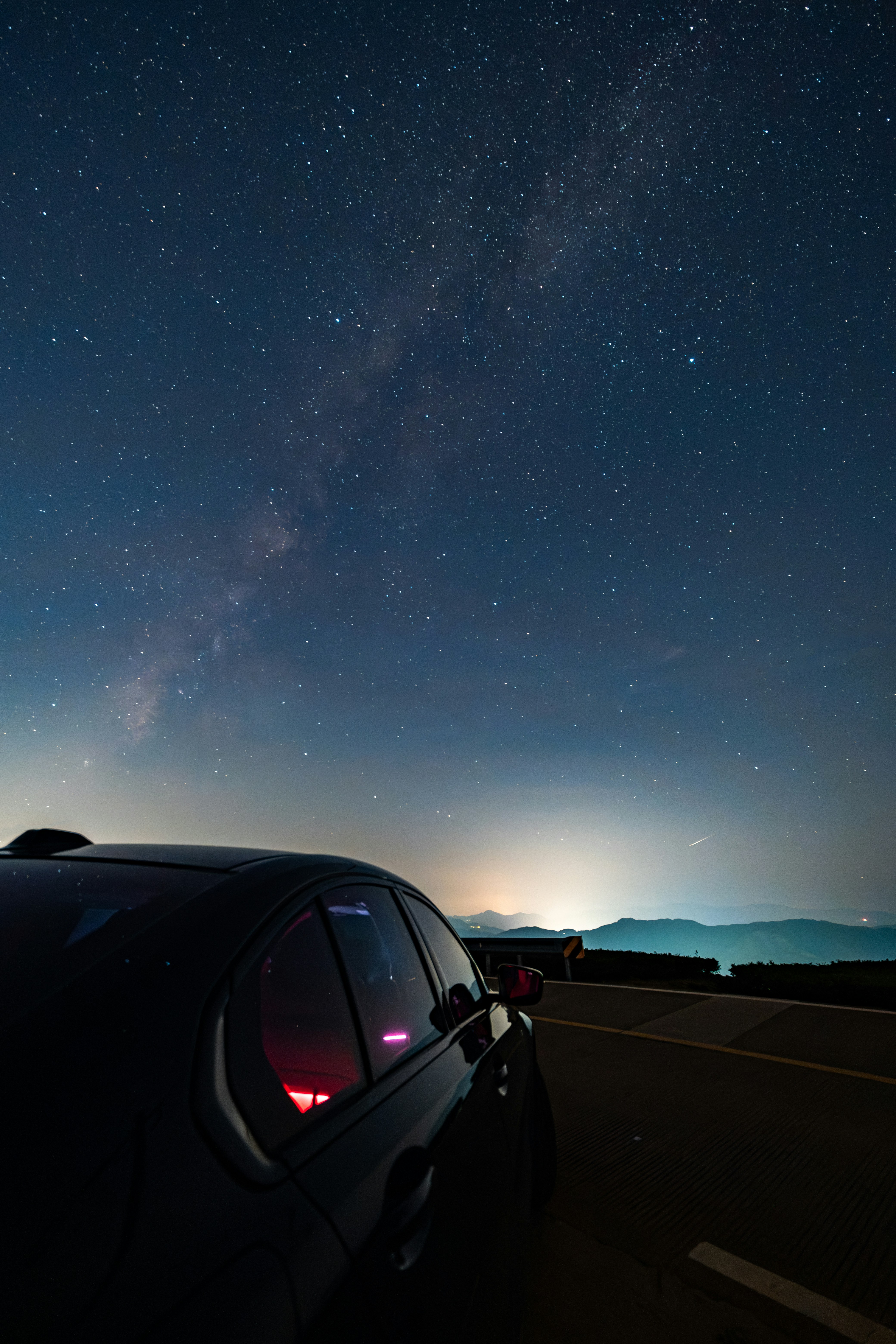 A car parked on the side of a road under a night sky filled with stars ...