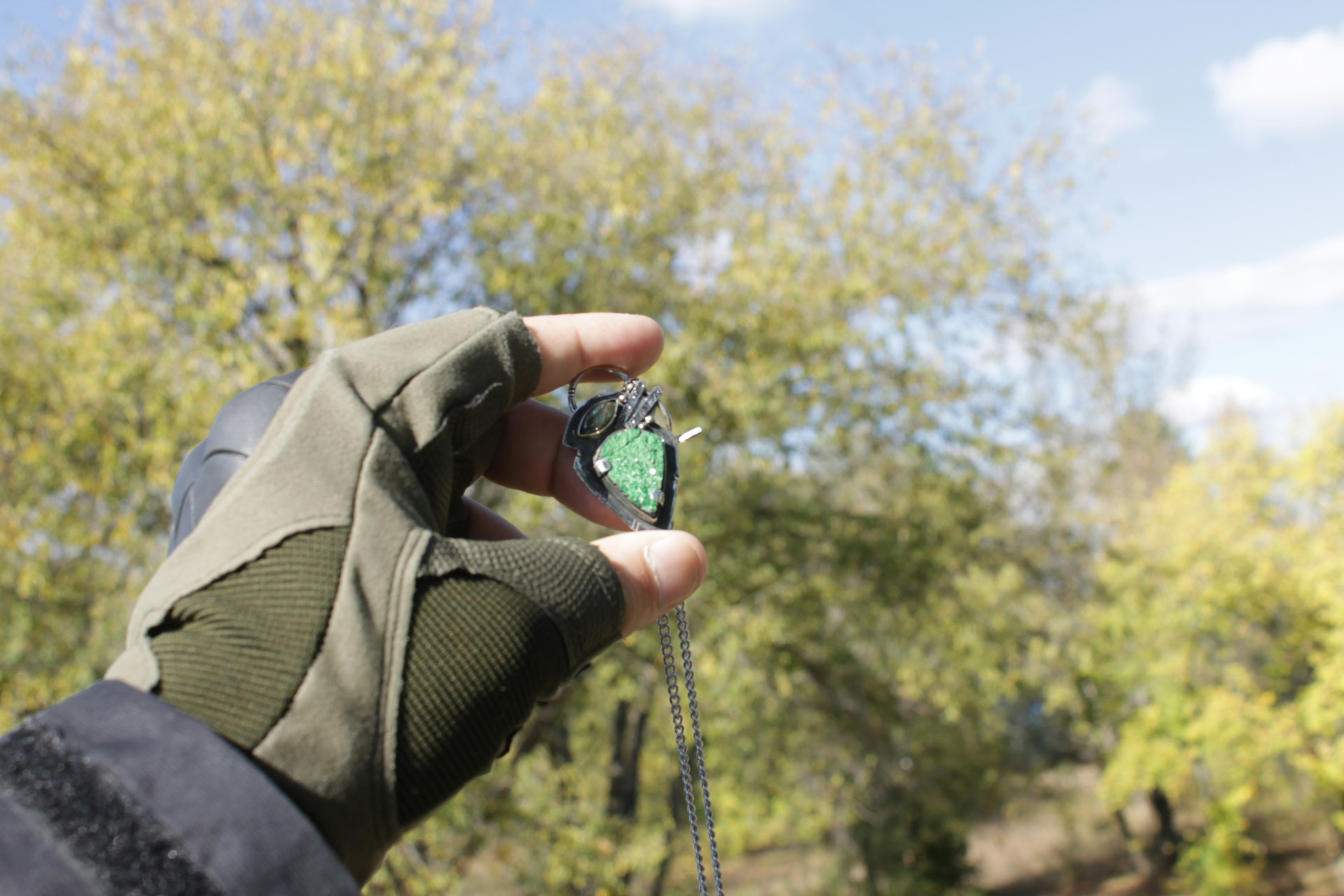 Glinting pendant held aloft against a sunlit grove