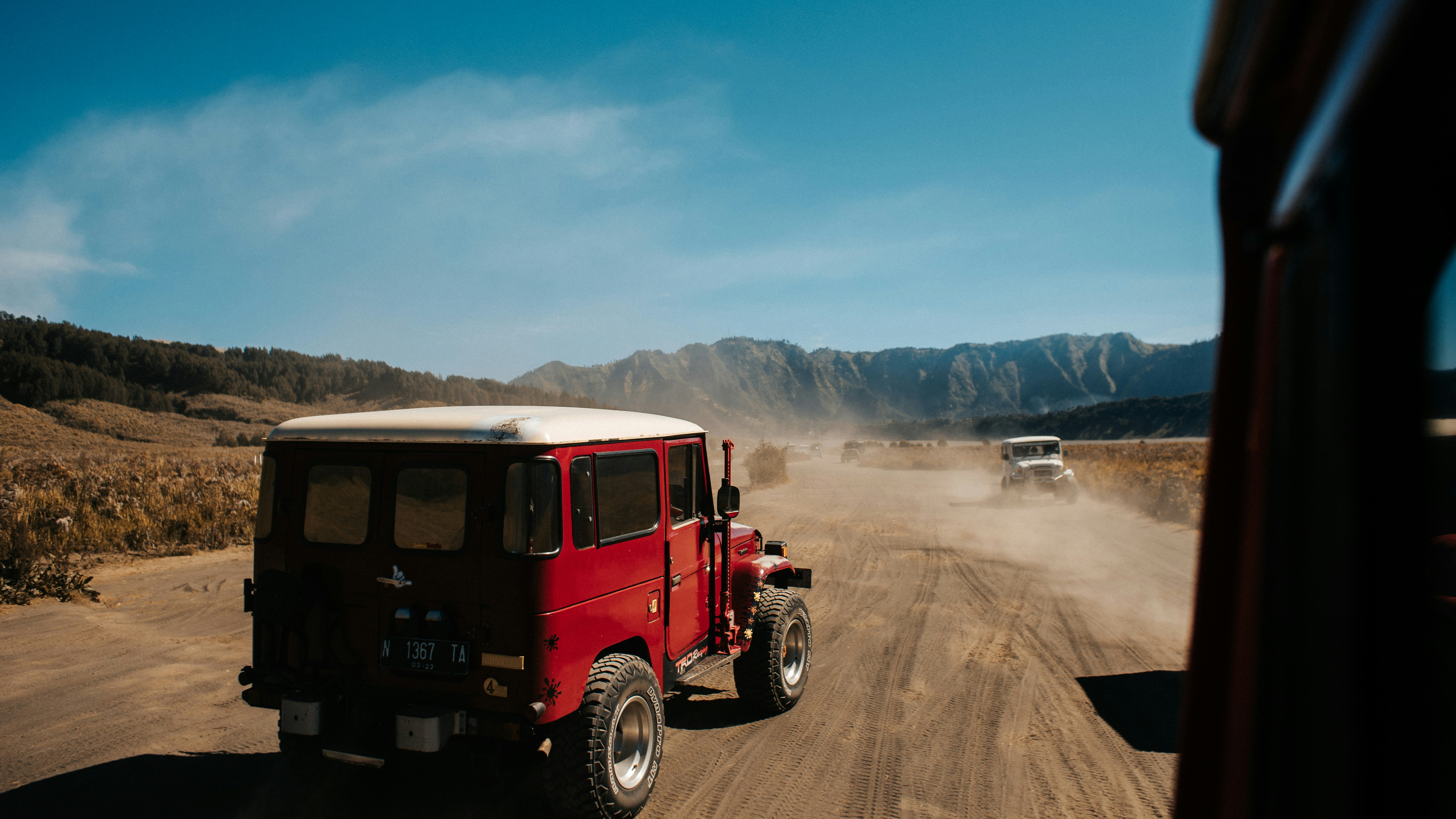 Dust Trail Pursuit: A Red Jeep on a Desert Road Toward the Mountain Verge