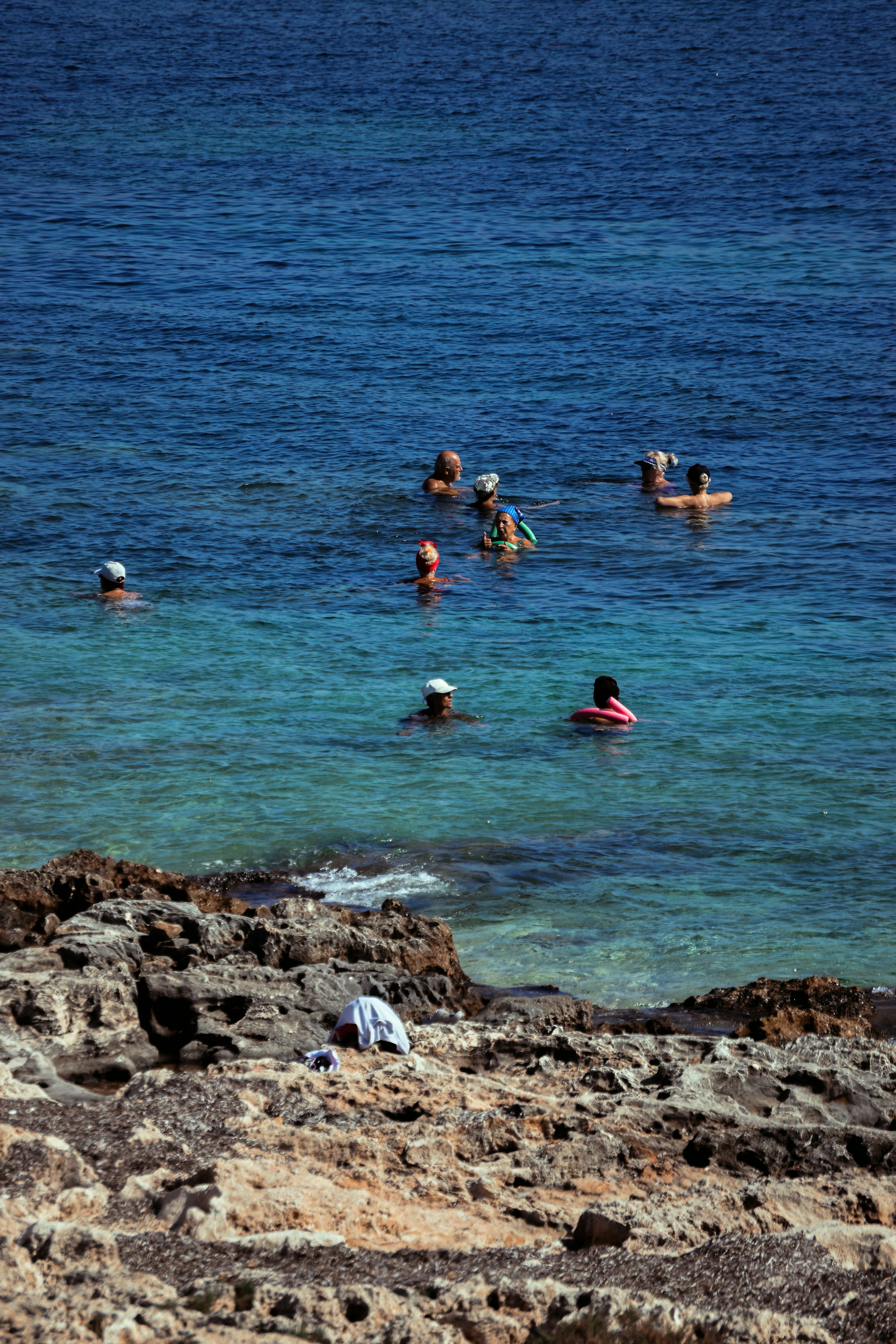 Sunlit Swell: People Enjoying Clear Blue Waters along a Rocky Shore