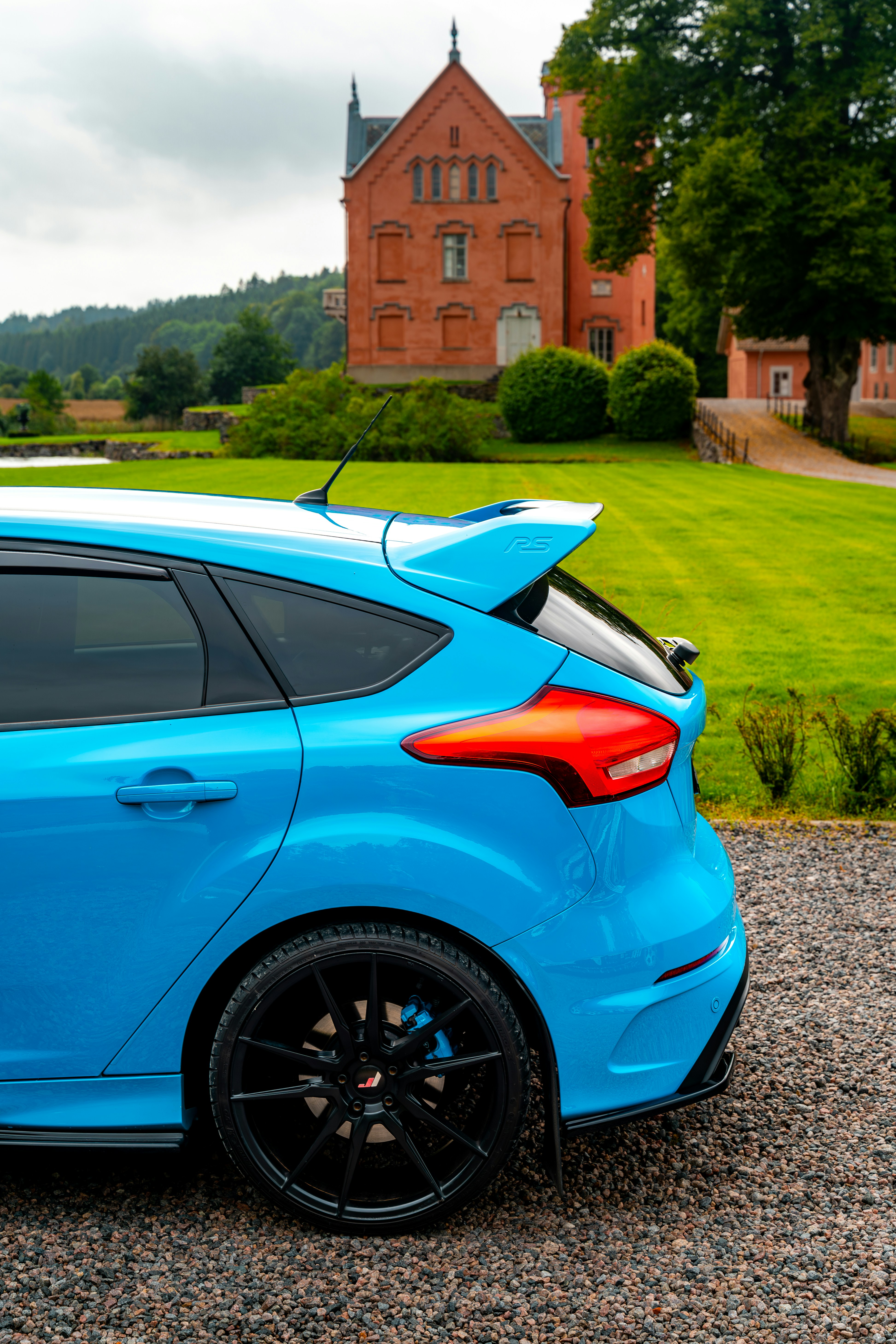 Blue hatchback in front of historic red-brick manor