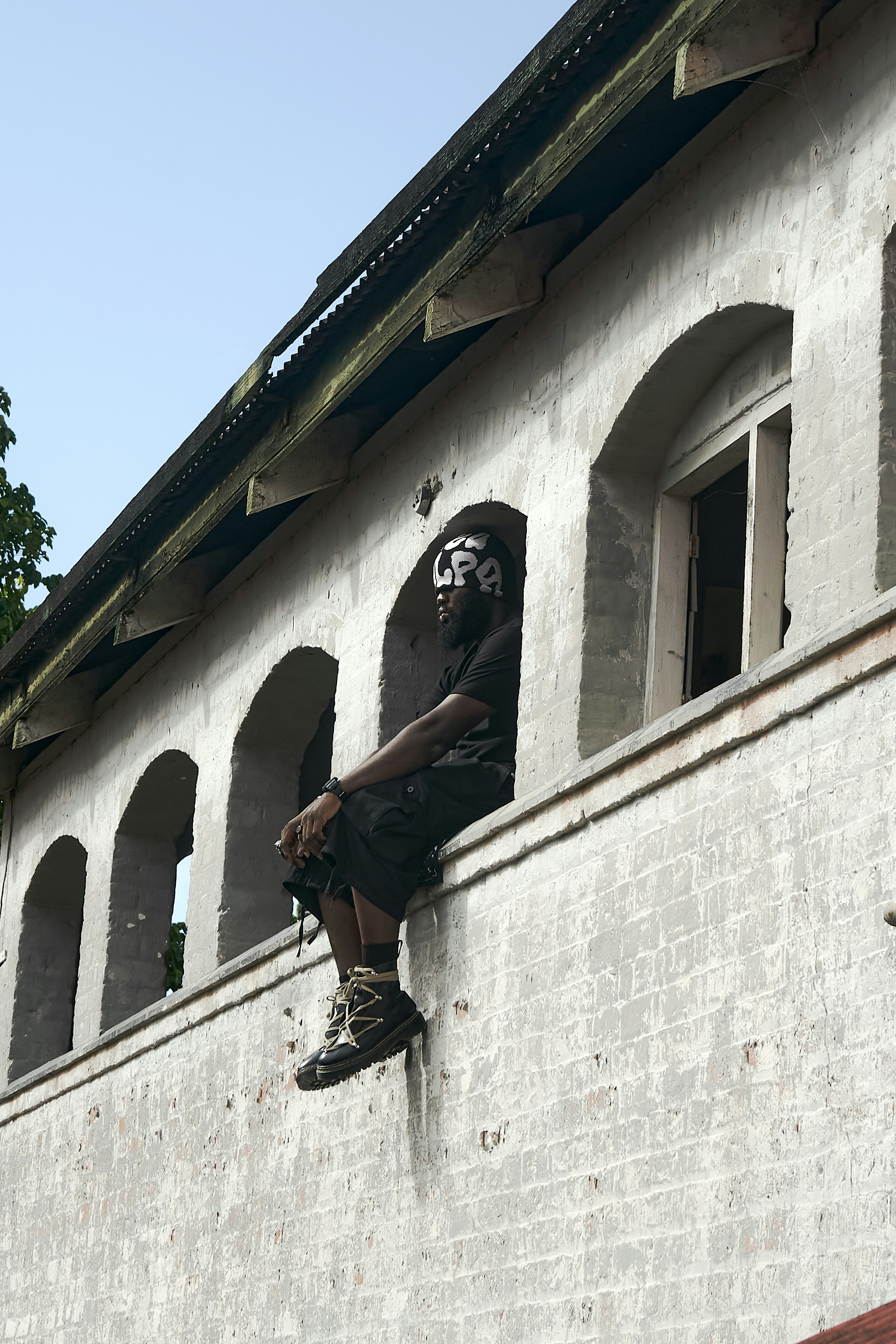 Perch Above the Arcade: A Shadowed Figure on a Weathered Wall