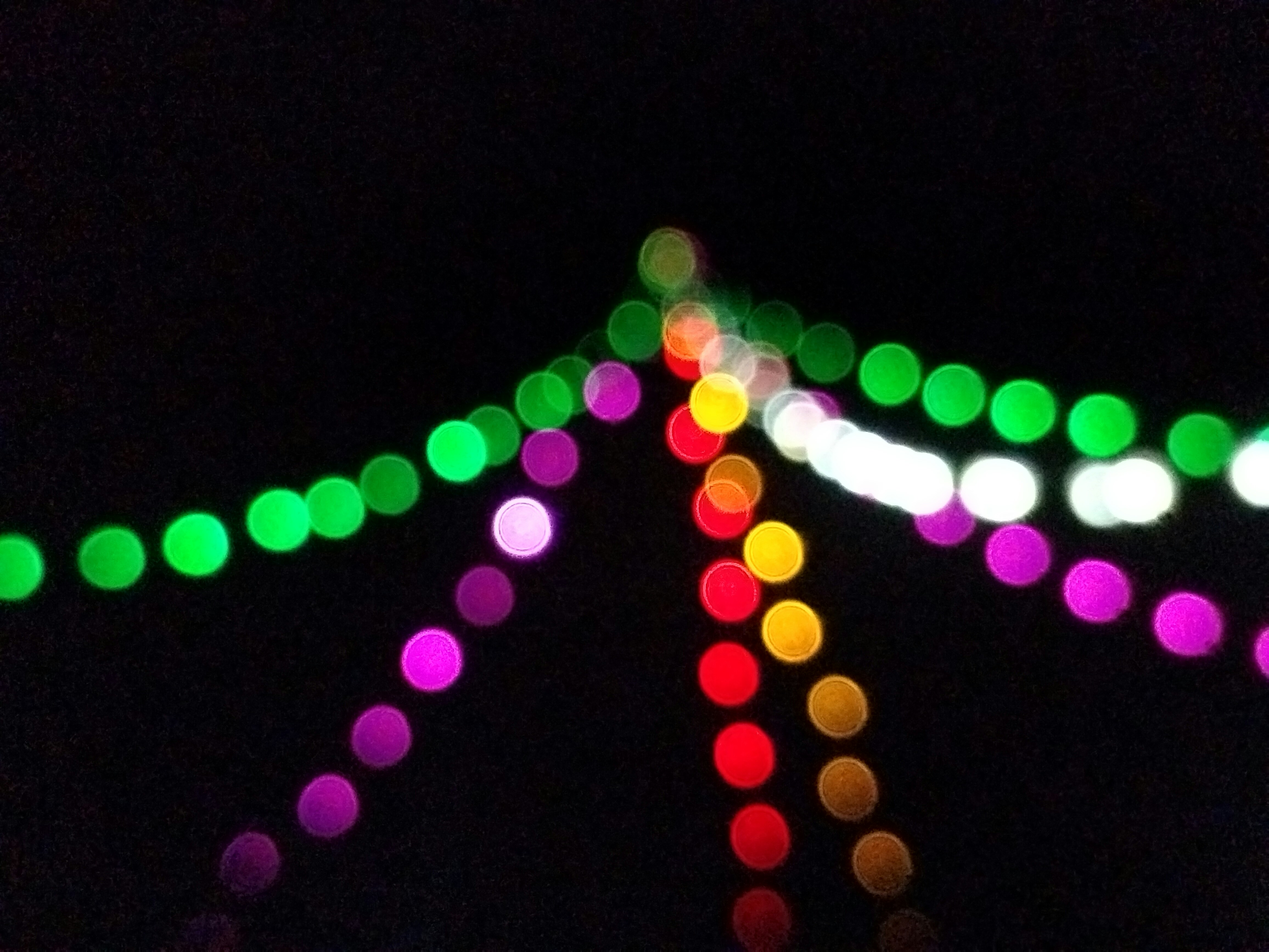 A photograph of colorful bokeh string lights converging toward a central apex against a dark sky. The vibrant orbs form geometric lines that guide the eye to the peak.