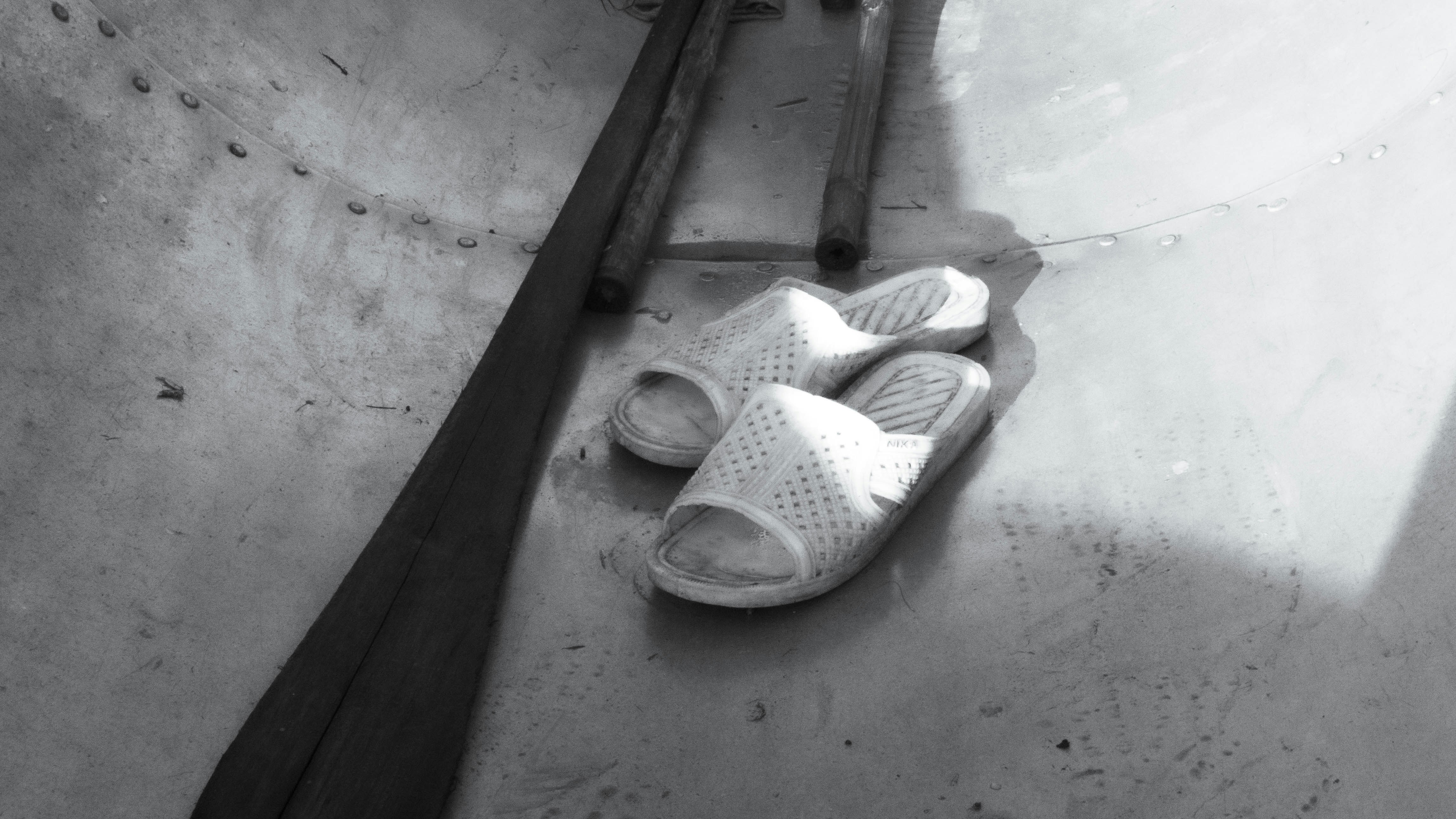 Two white sandals sit abandoned inside a curved metal slide, captured in grayscale.