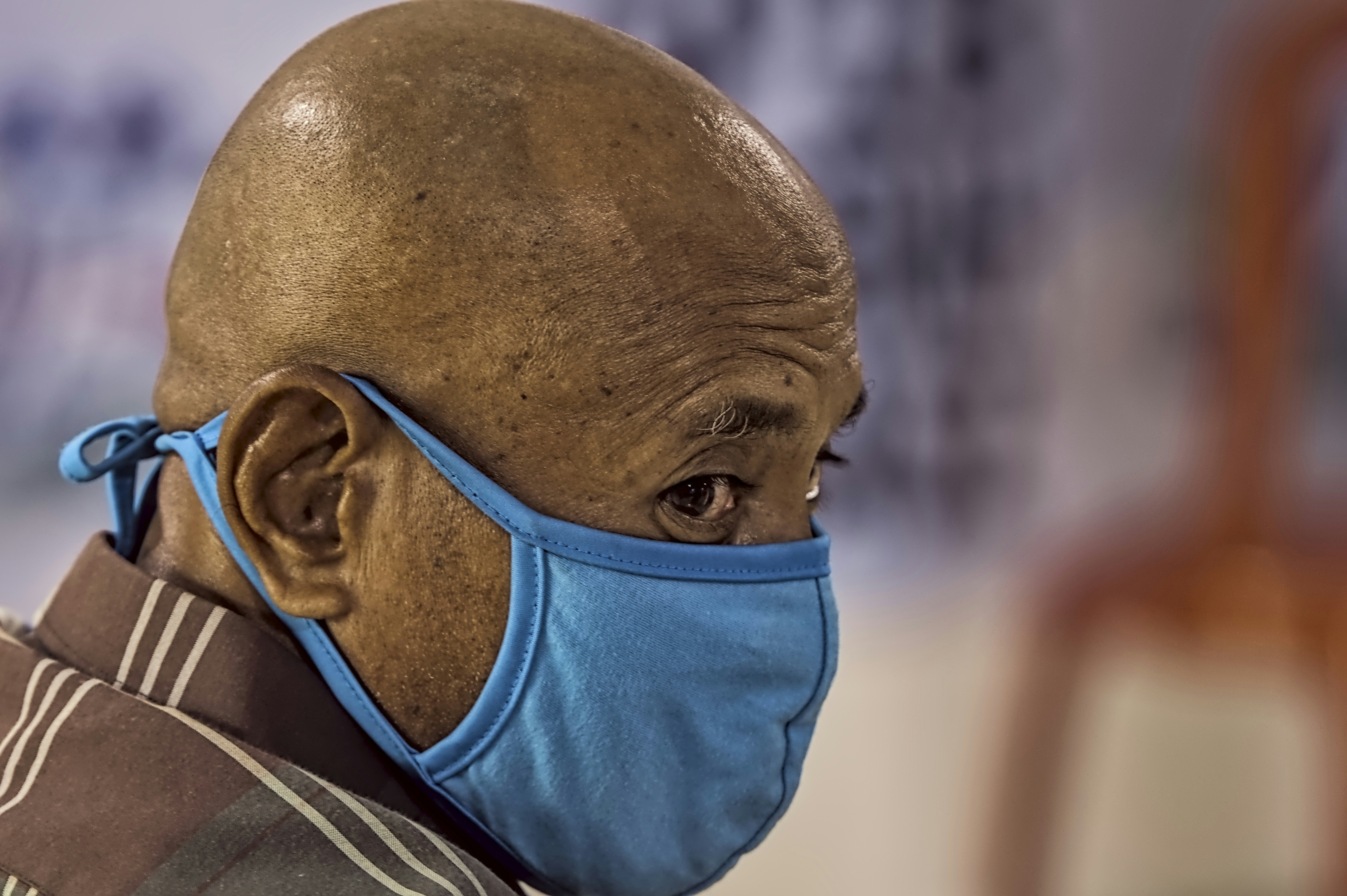 Man wearing a blue mask looks contemplatively to the side, with a blurred background.
