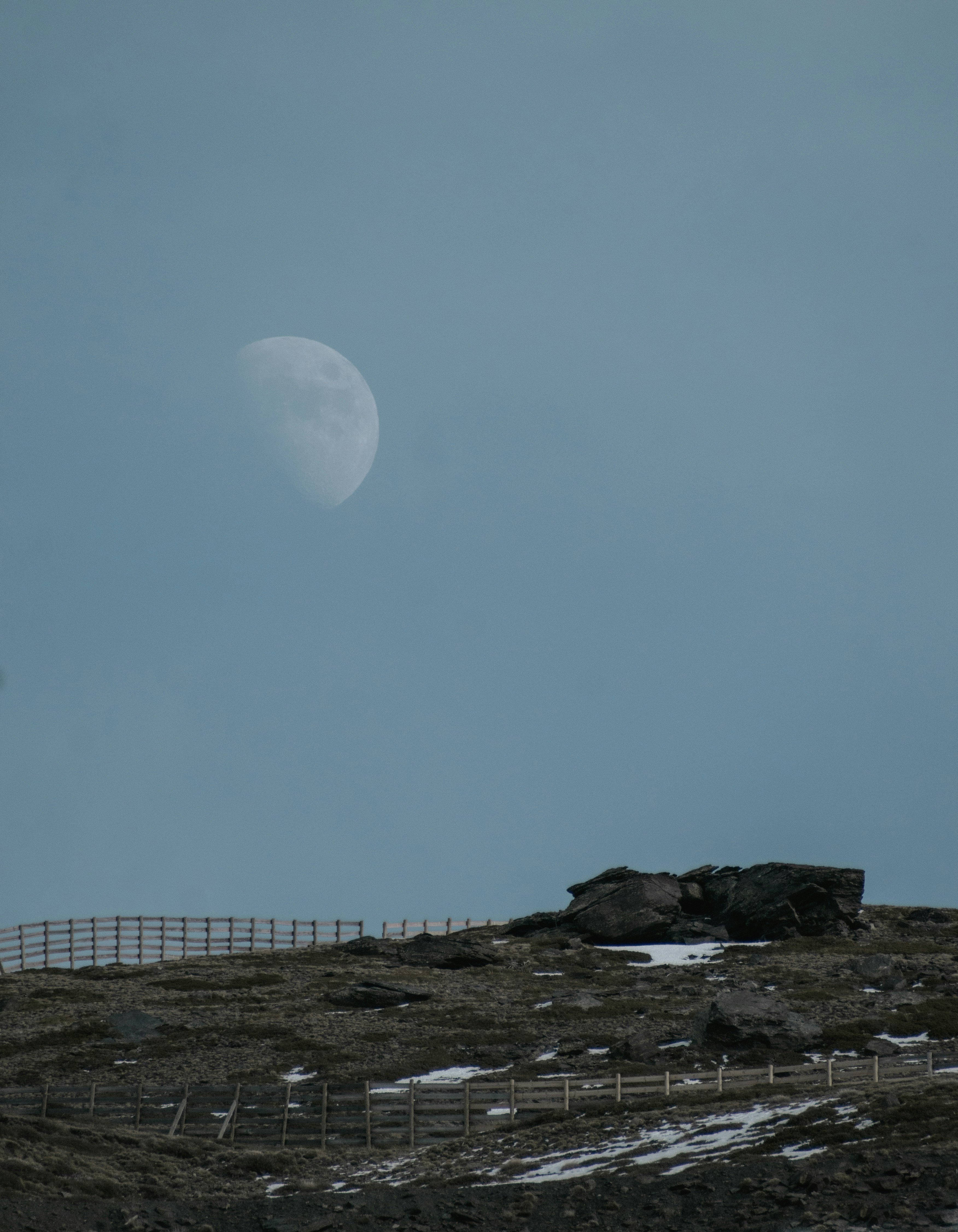Moon over a windswept rocky ridge with a weathered fence