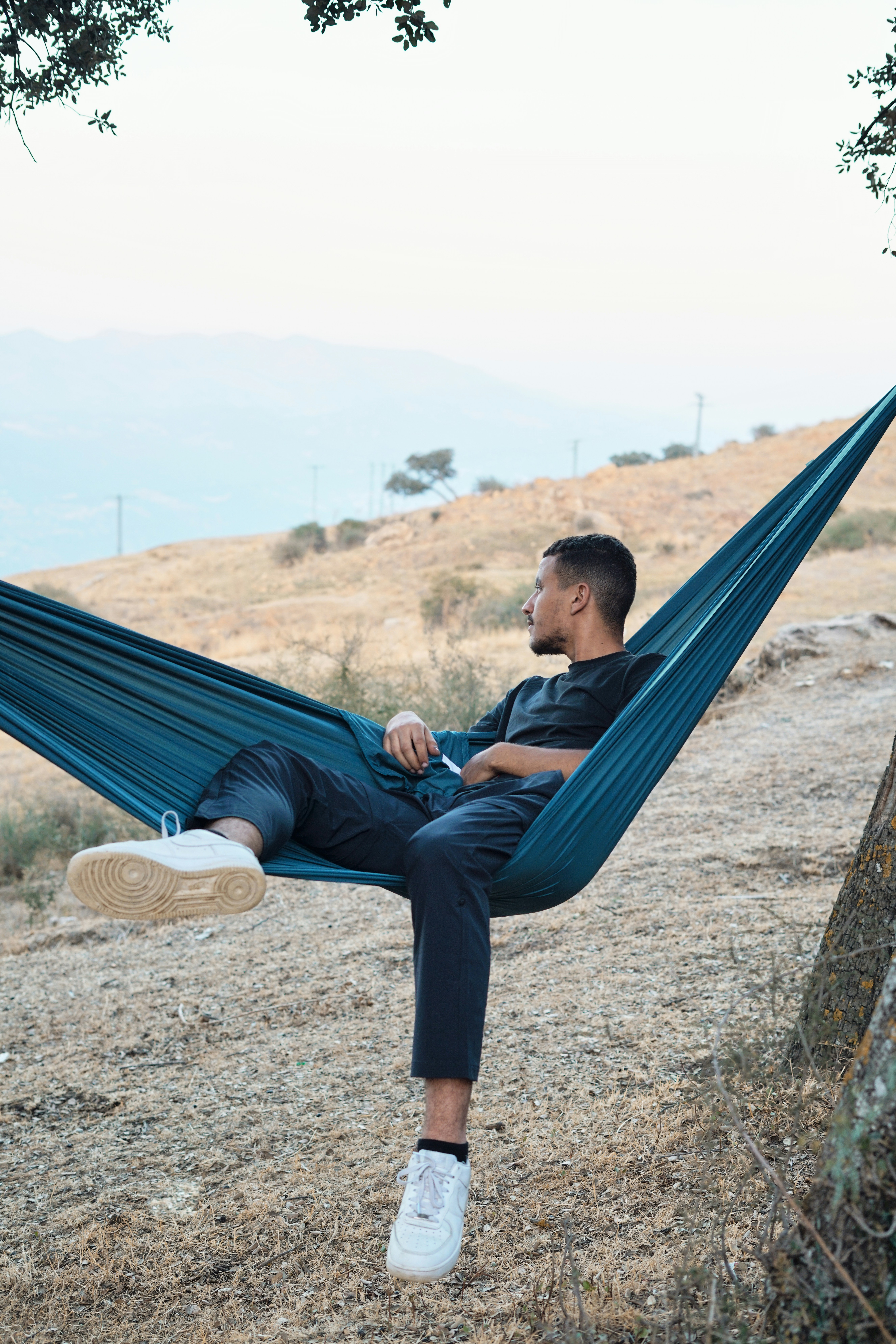 Man relaxing in a blue hammock amidst an arid landscape under a clear sky.