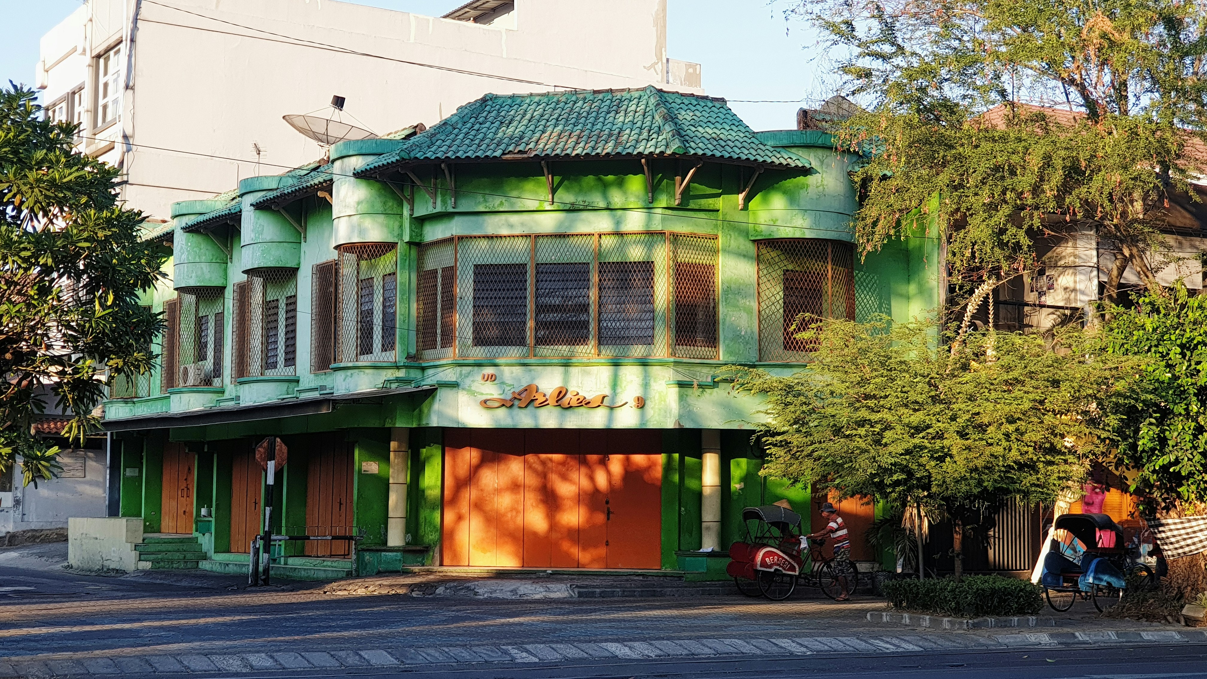 Green Art-Deco Streetfront with Orange Roll-Up Door, Sunlit in a Quiet Street